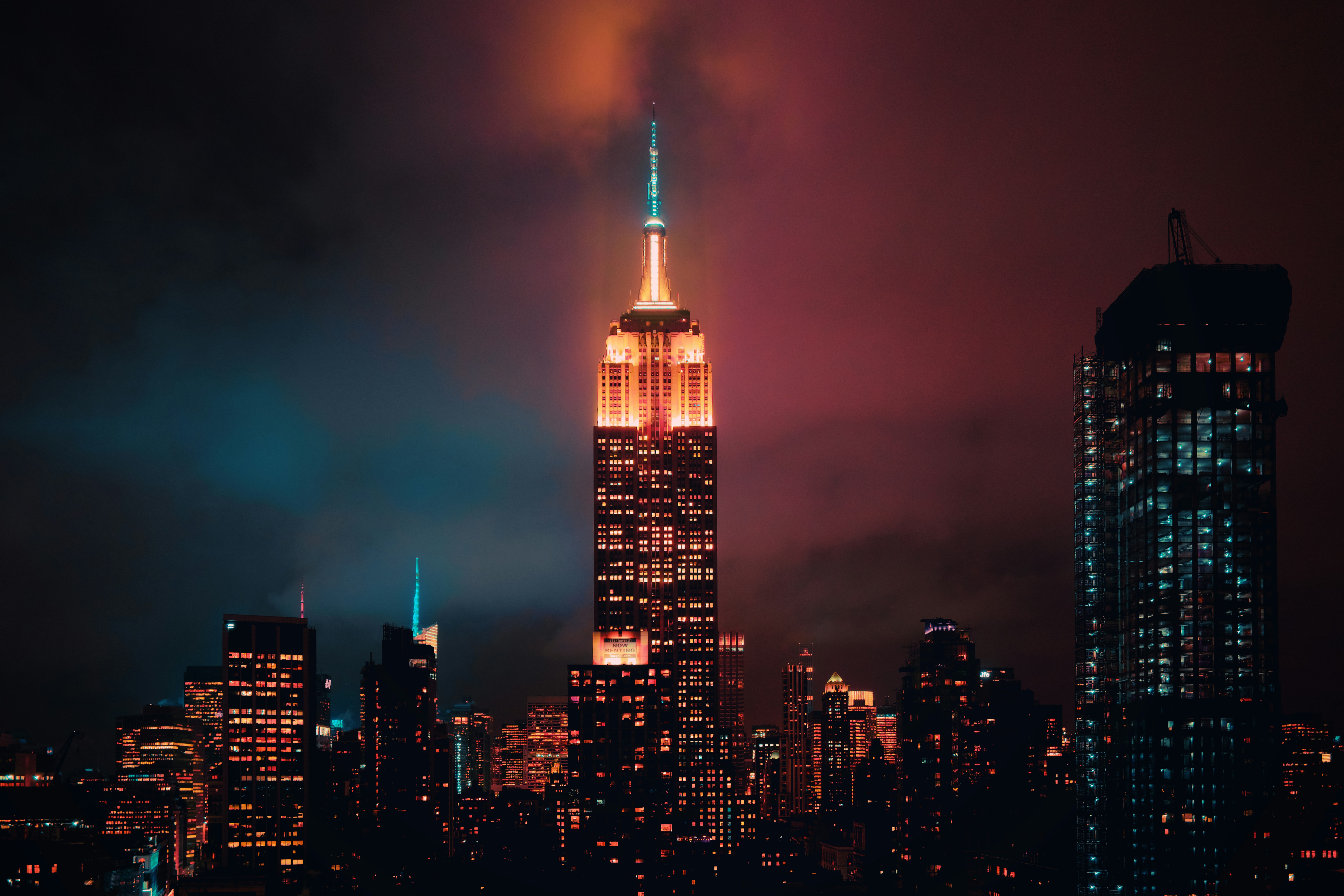 Empire State Building bathed in vibrant lights against a moody skyline, showcasing the architectural marvel amidst a dramatic evening backdrop.