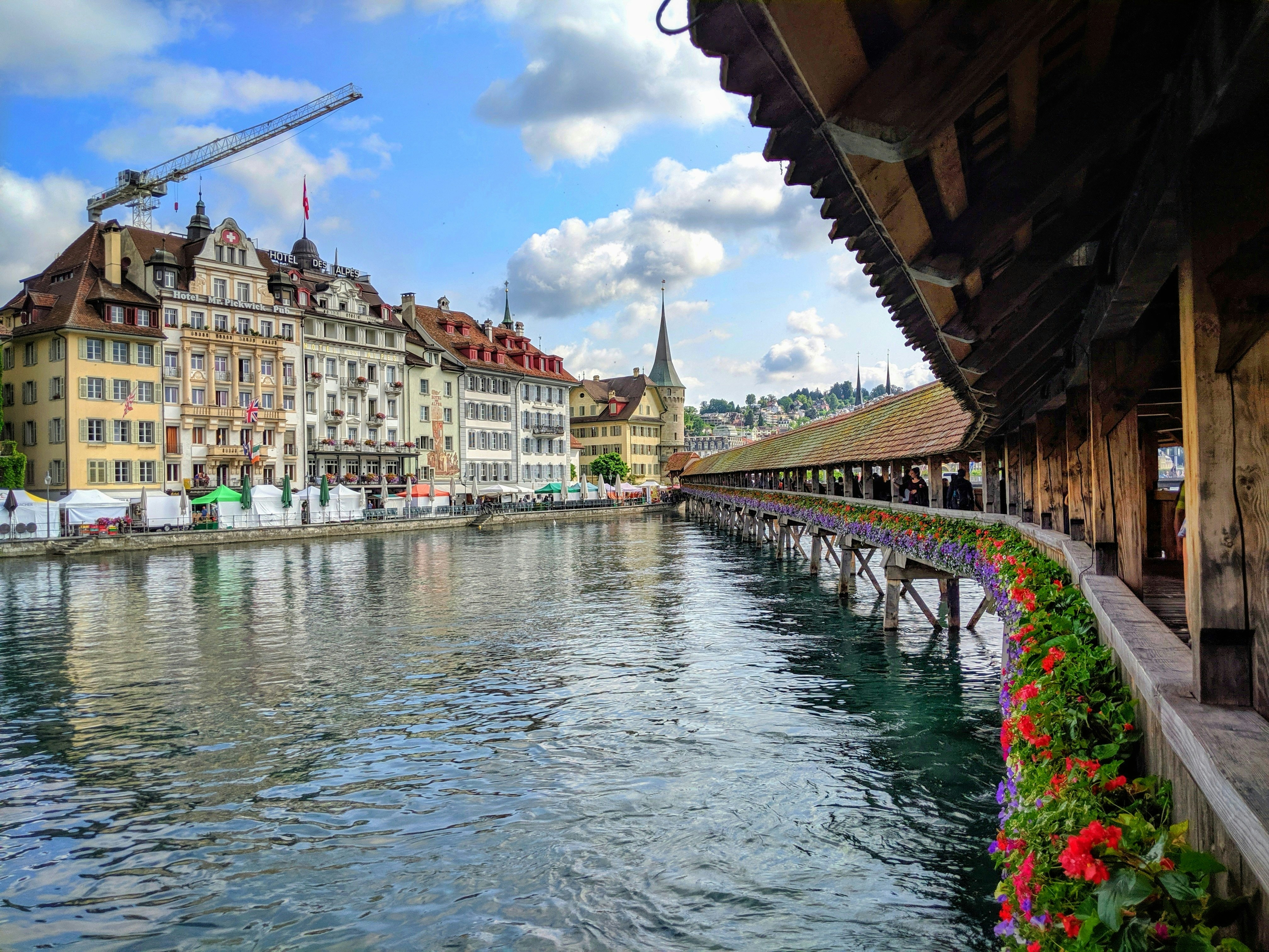 Colorful buildings and a historic wooden bridge line a calm river under a partly cloudy sky.