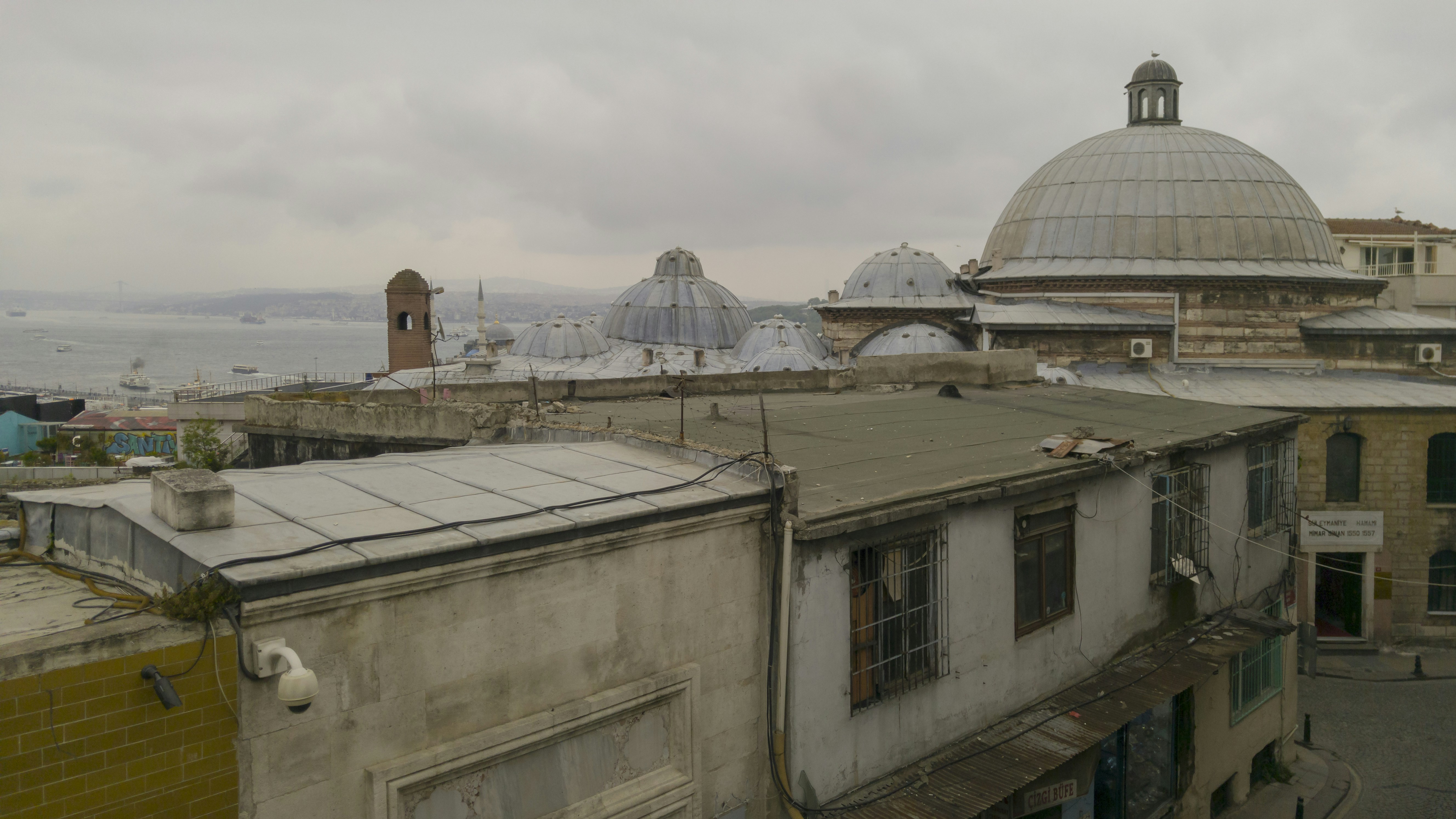 Historic domes and rooftops of Istanbul's old buildings overlooking the Bosphorus, captured on a cloudy day.