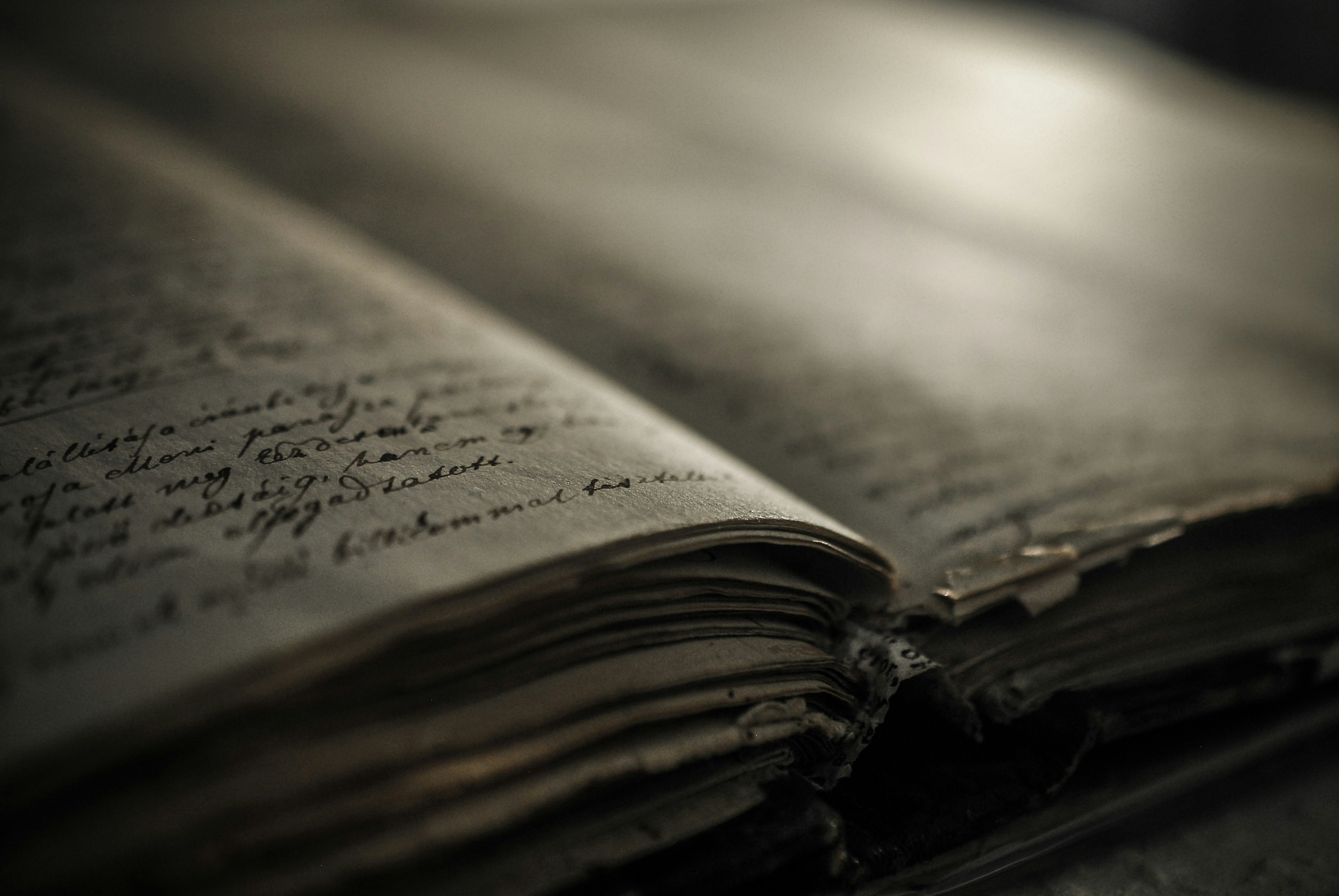 Close-up of an aged book with handwritten notes on its pages, softly lit in a dim setting.
