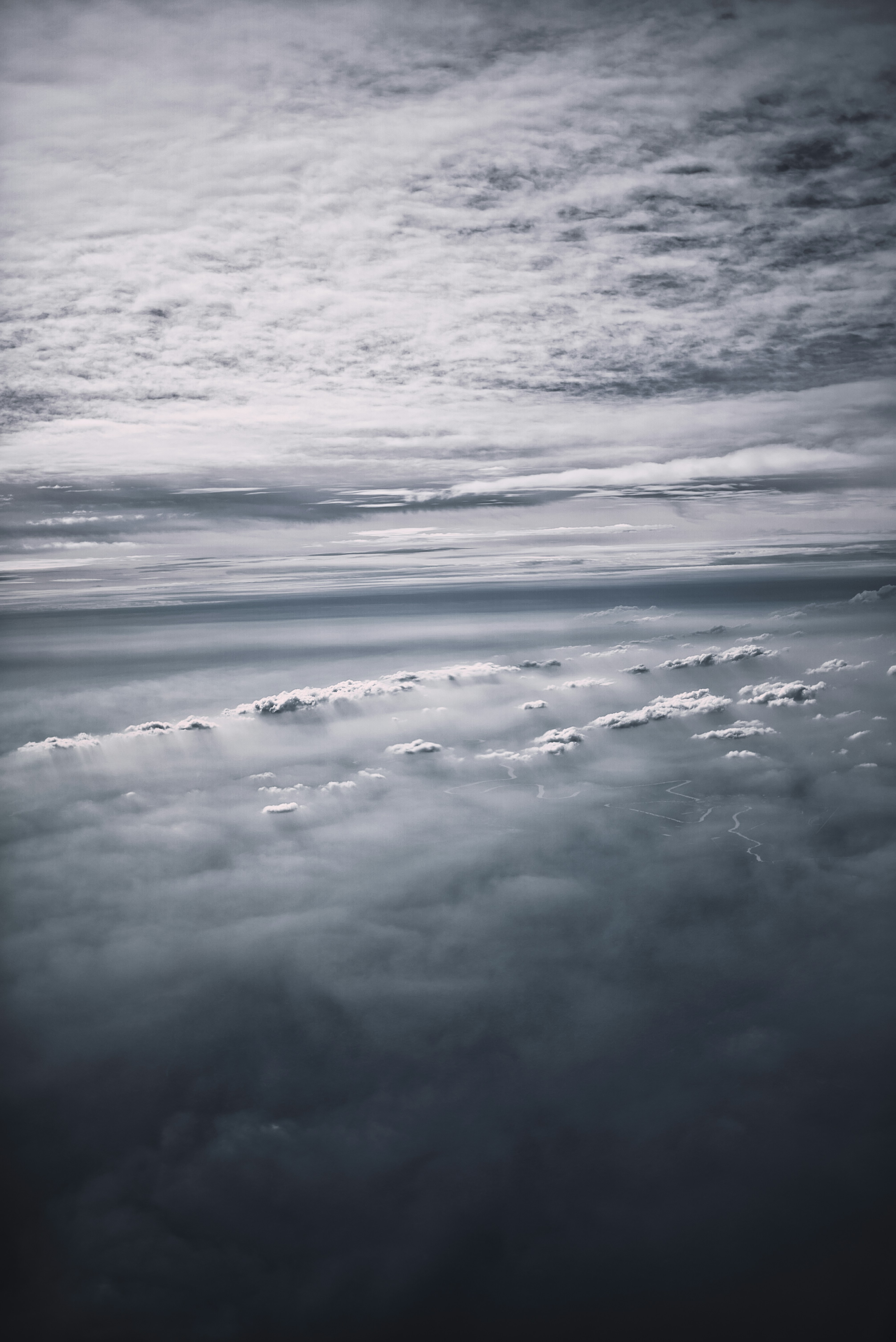 Expansive view of layered clouds beneath a textured sky, captured in monochrome tones. The scene evokes a sense of tranquility and vastness.