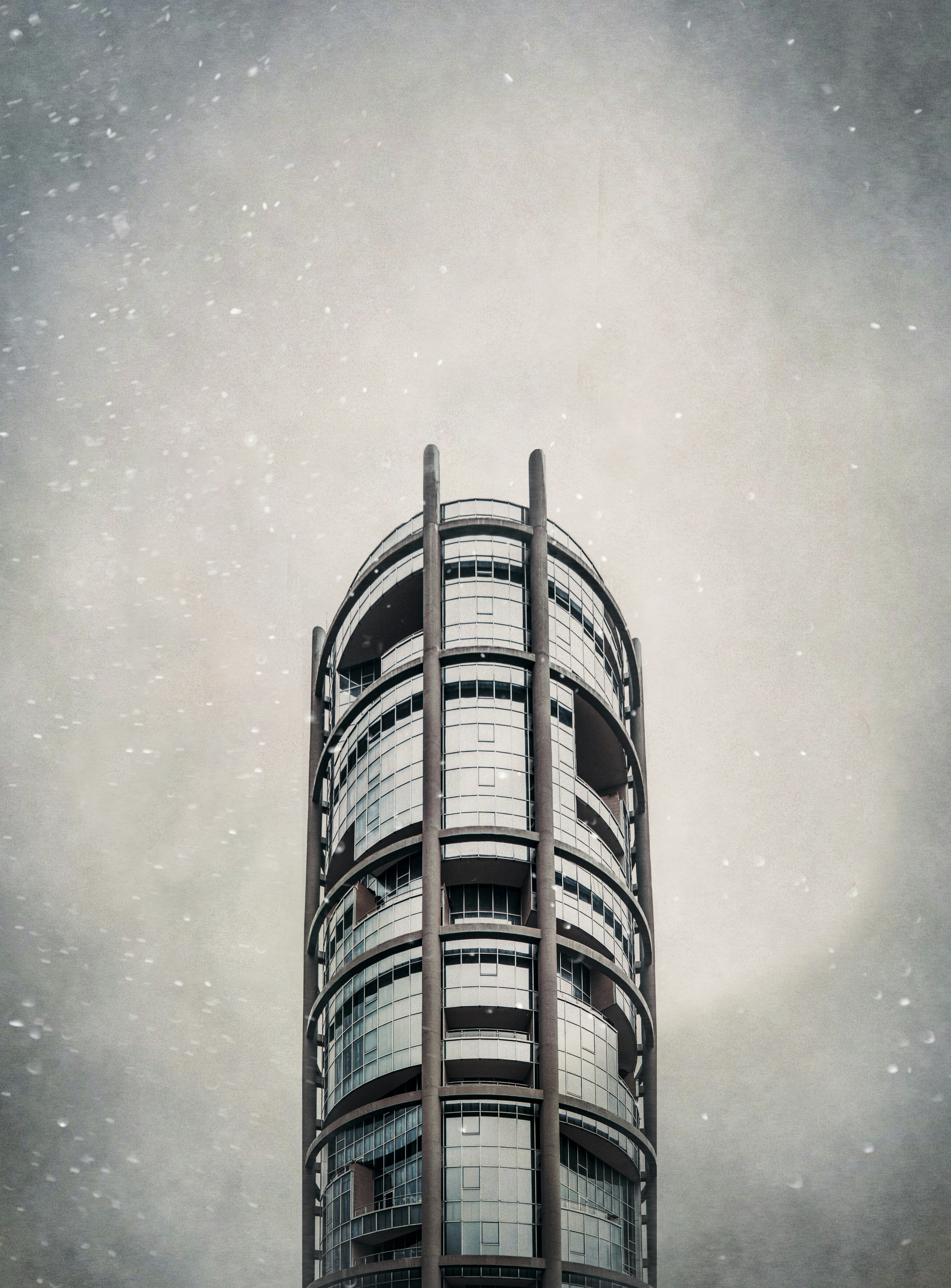 Sleek modern tower rises against a muted sky, dusted with snowflakes, showcasing architectural design and urban resilience.