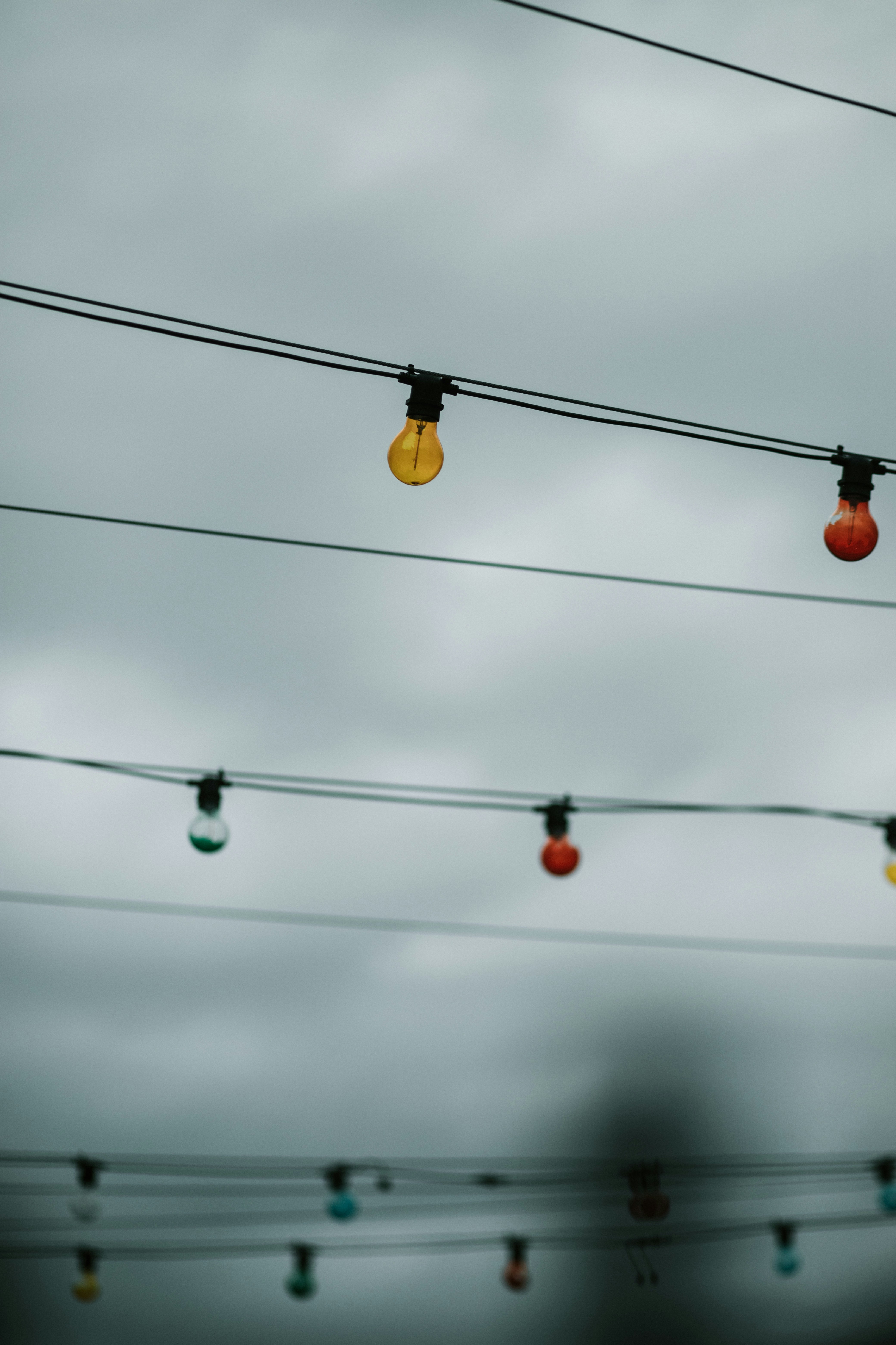 Colorful string lights hanging against a cloudy sky, creating a whimsical contrast in a moody atmosphere.