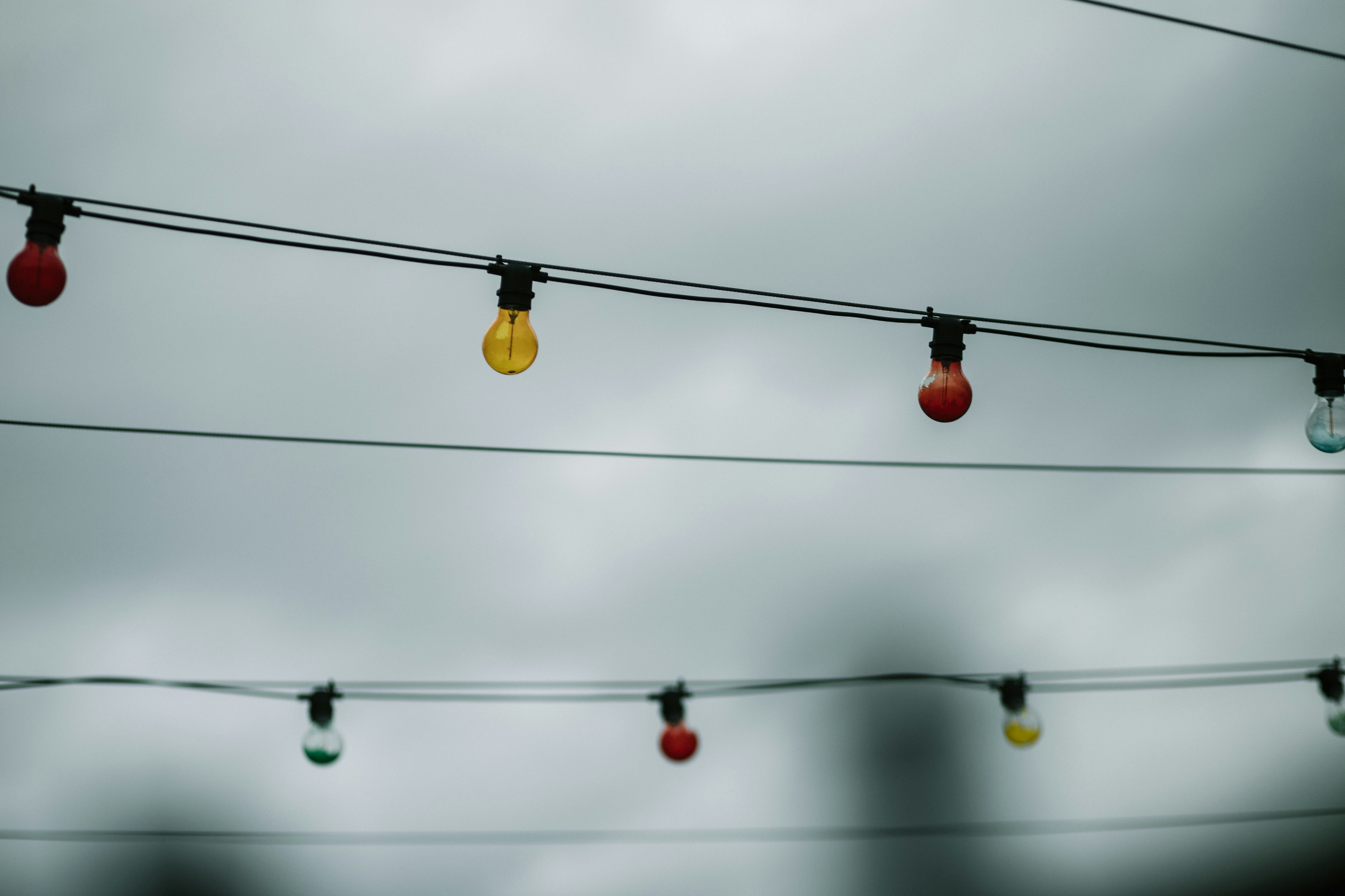 Colorful string lights hanging against a cloudy sky, creating a contrast between brightness and overcast ambiance.