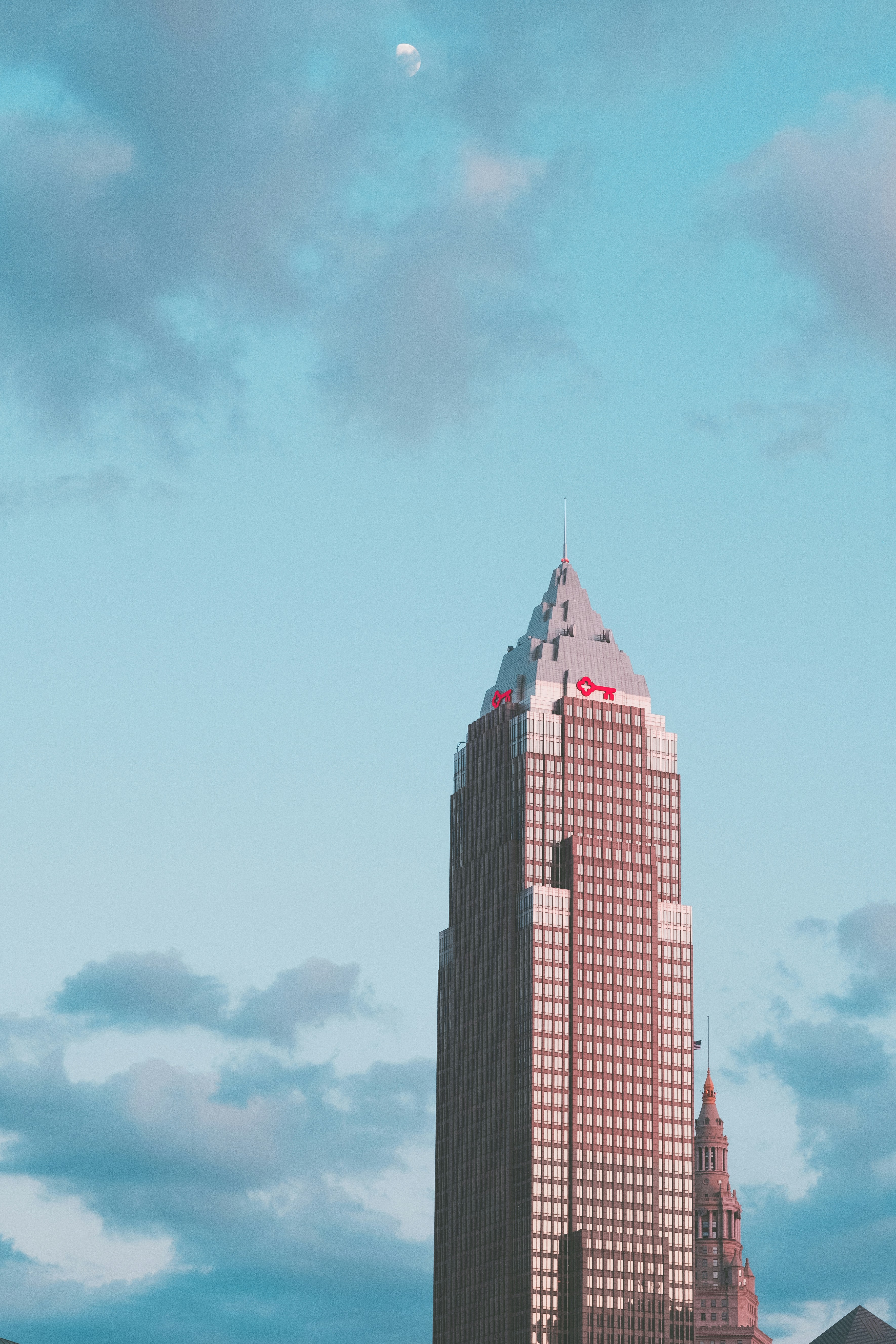 The towering Key Tower in Cleveland stands prominently against a serene sky, with soft clouds and a hint of moonlight above. The architectural details reflect the city's unique skyline.