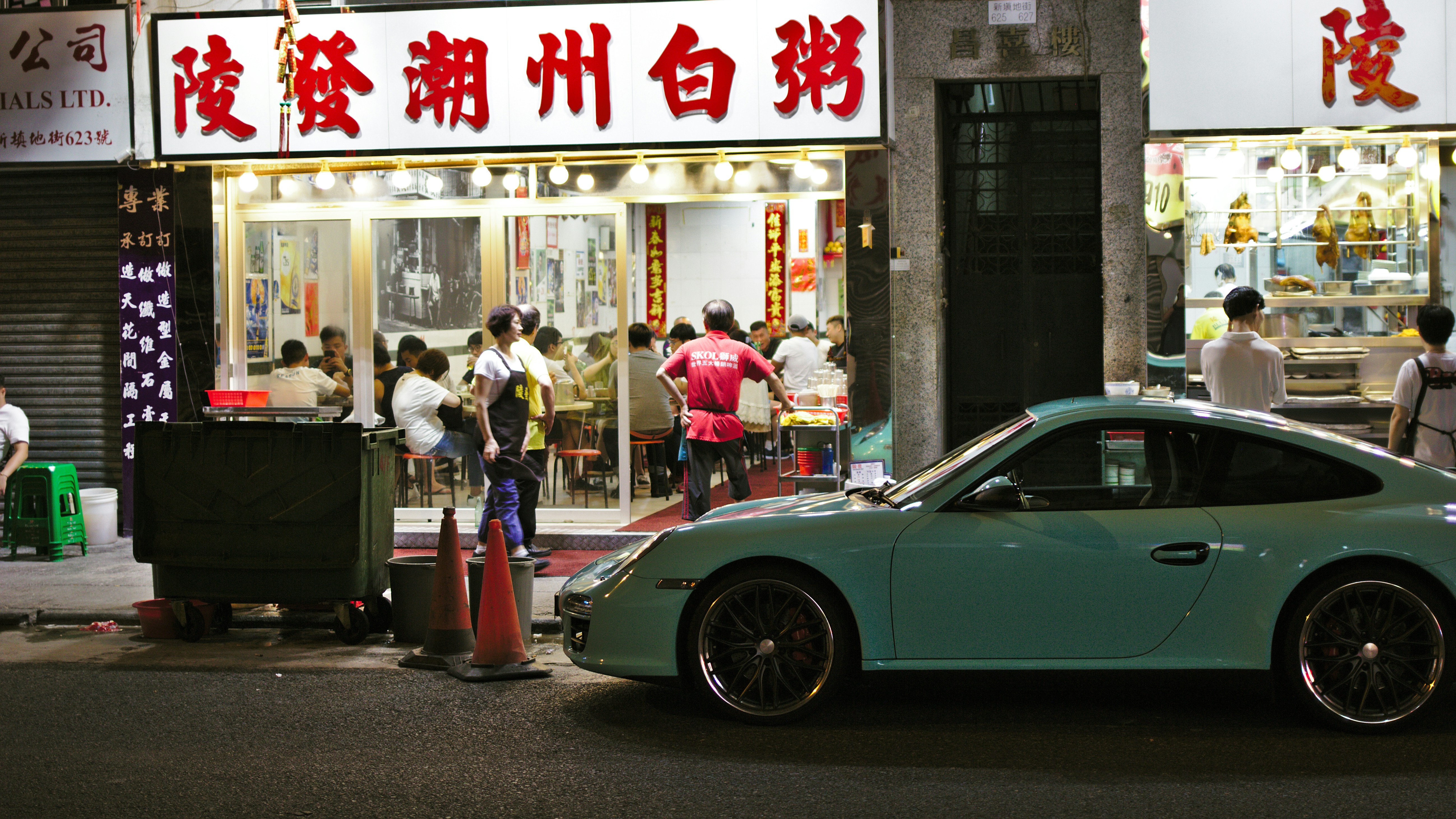 Neon-lit Chinatown Street: Turquoise Sports Car Beside a Bustling Night Market