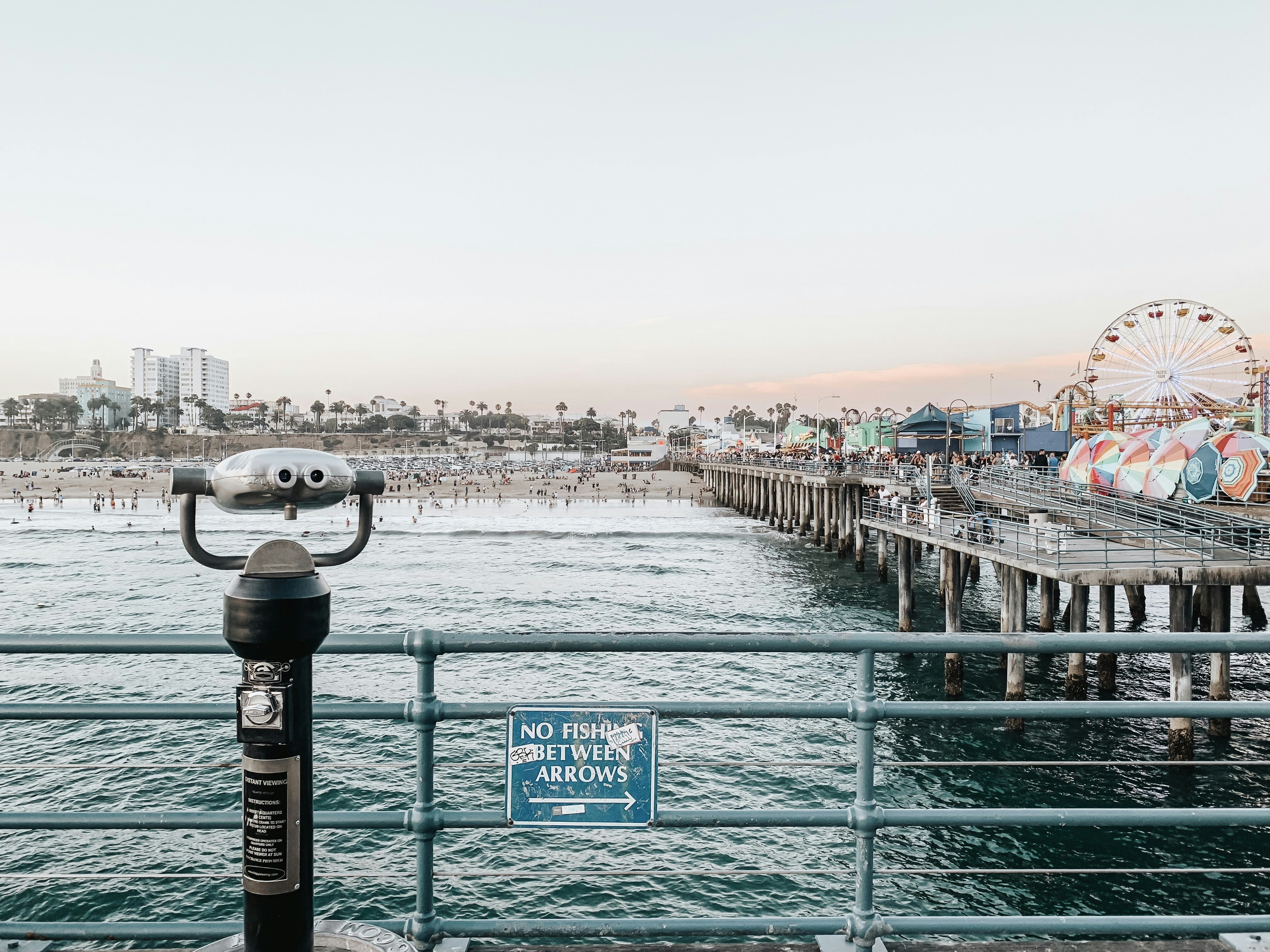 Observation binoculars overlooking a bustling pier with a distant ferris wheel at sunset.