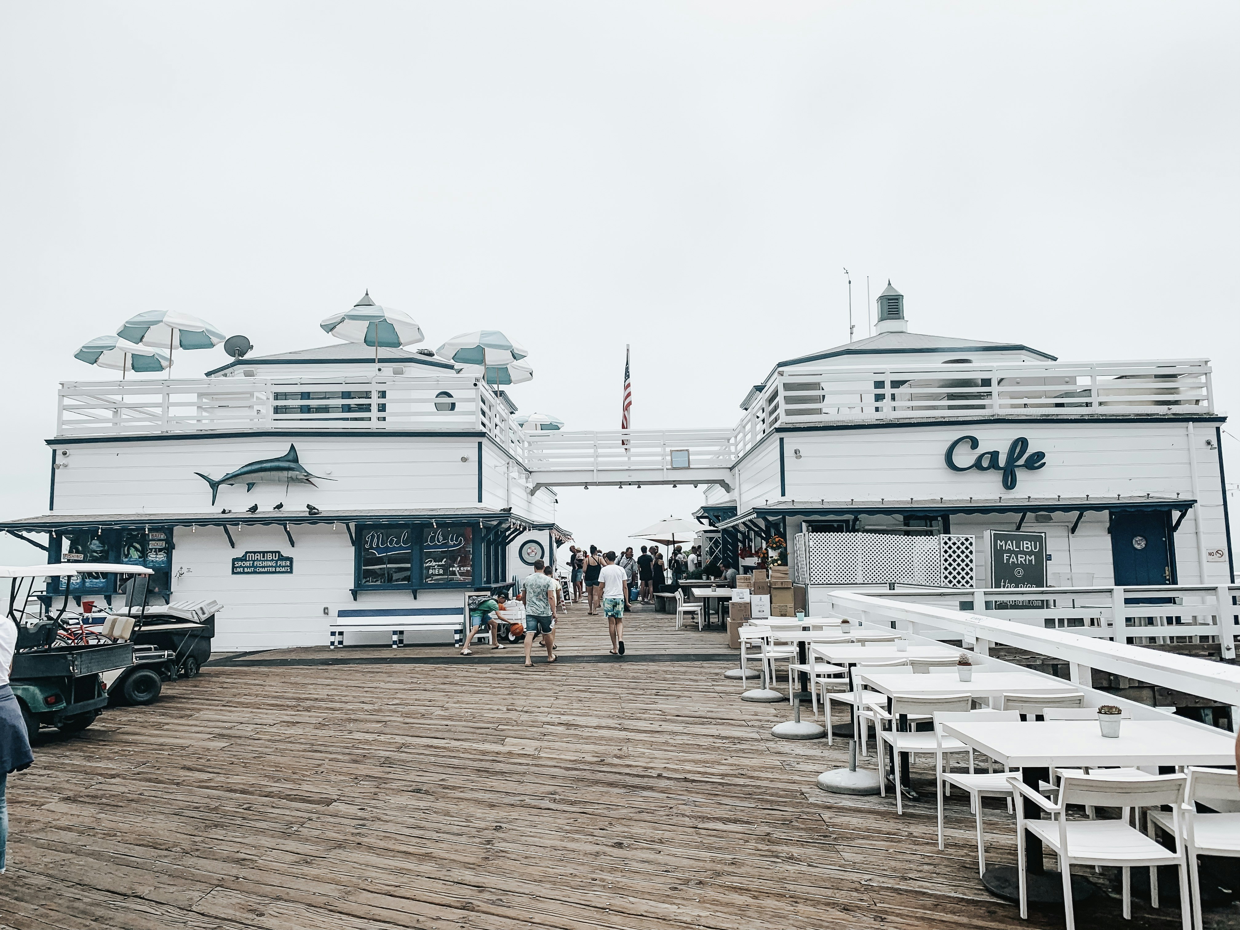 Sunlit Pierfront Café Row: Whitewashed Huts Framing a Central Crowd on the Boardwalk