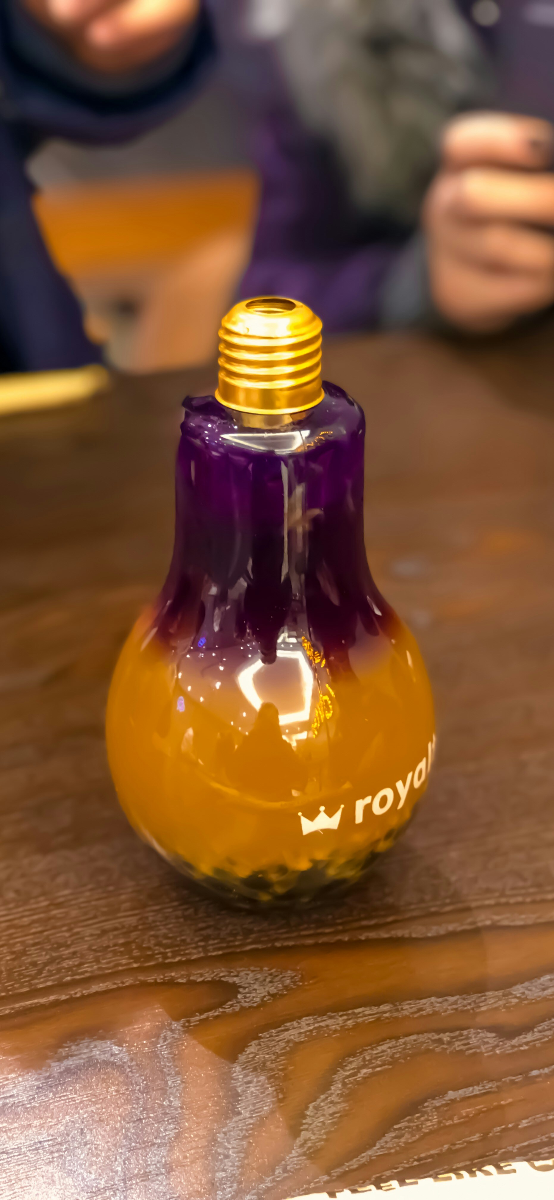 Vibrant glass bottle with a gradient of purple and orange, featuring a gold cap and the word 'royal' etched on the side.