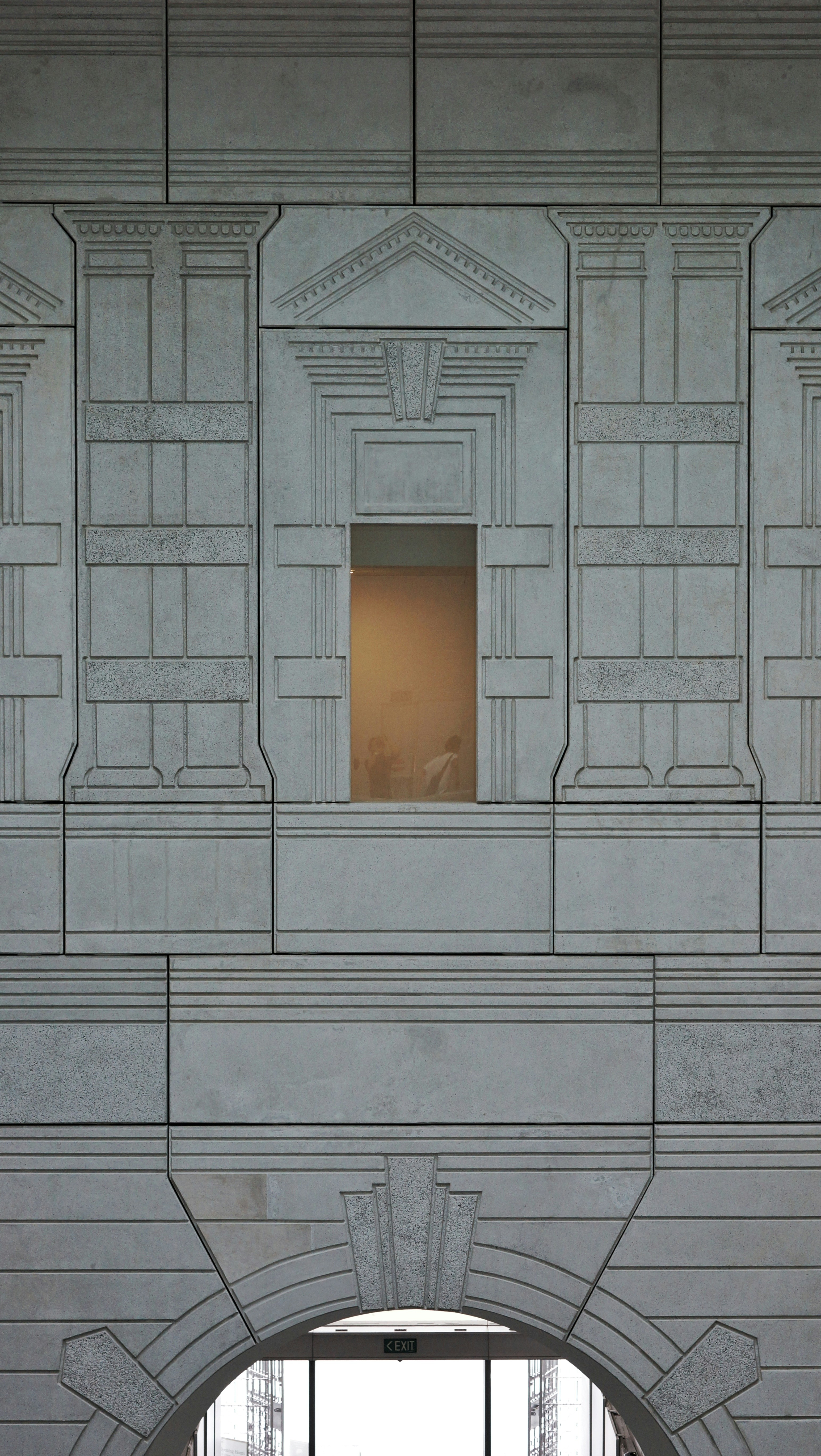 Minimalist architectural facade featuring a centrally placed window that offers a glimpse into the interior, surrounded by intricate detailing.