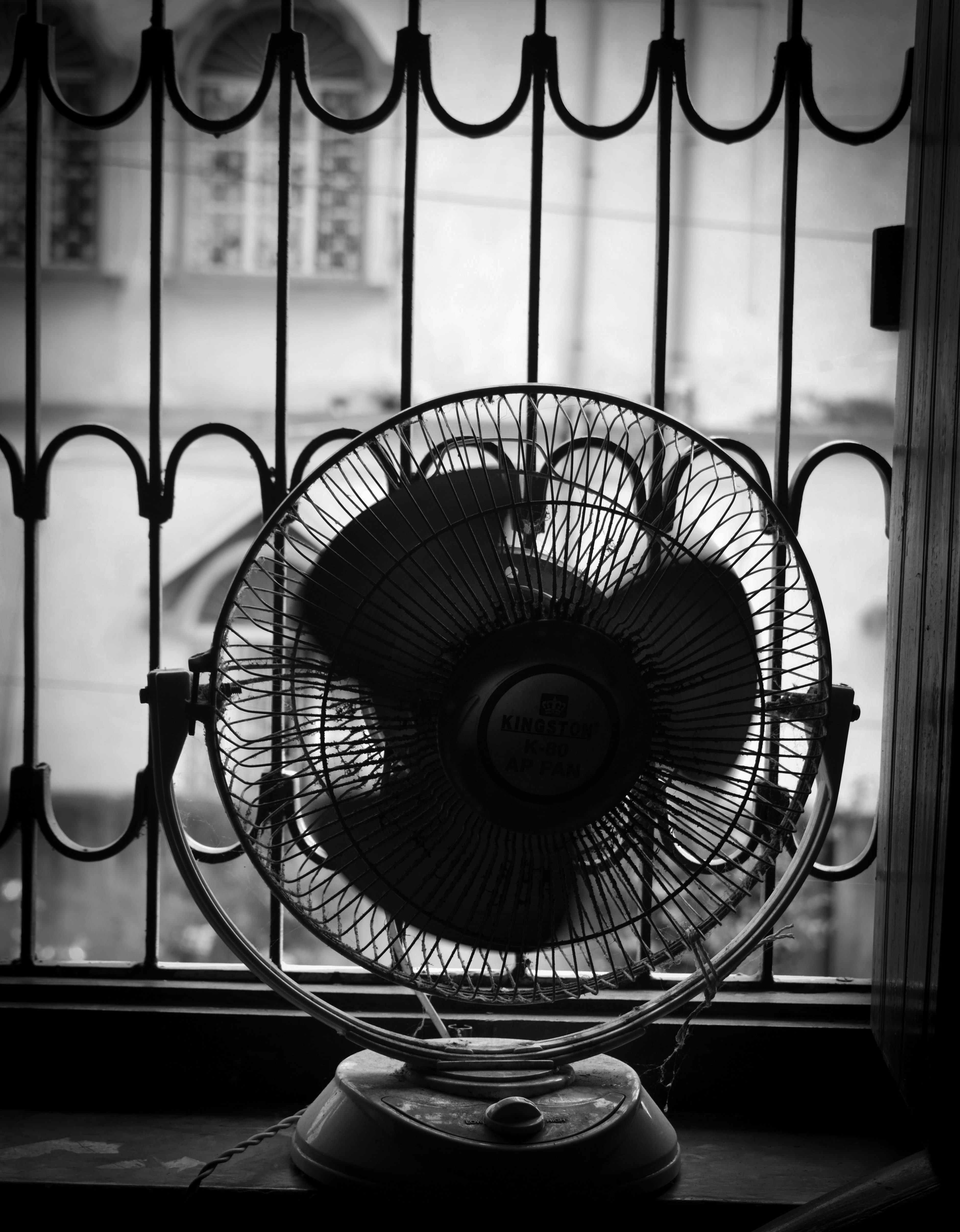 Vintage fan silhouetted against a softly blurred window, capturing a moment of nostalgia in black and white.