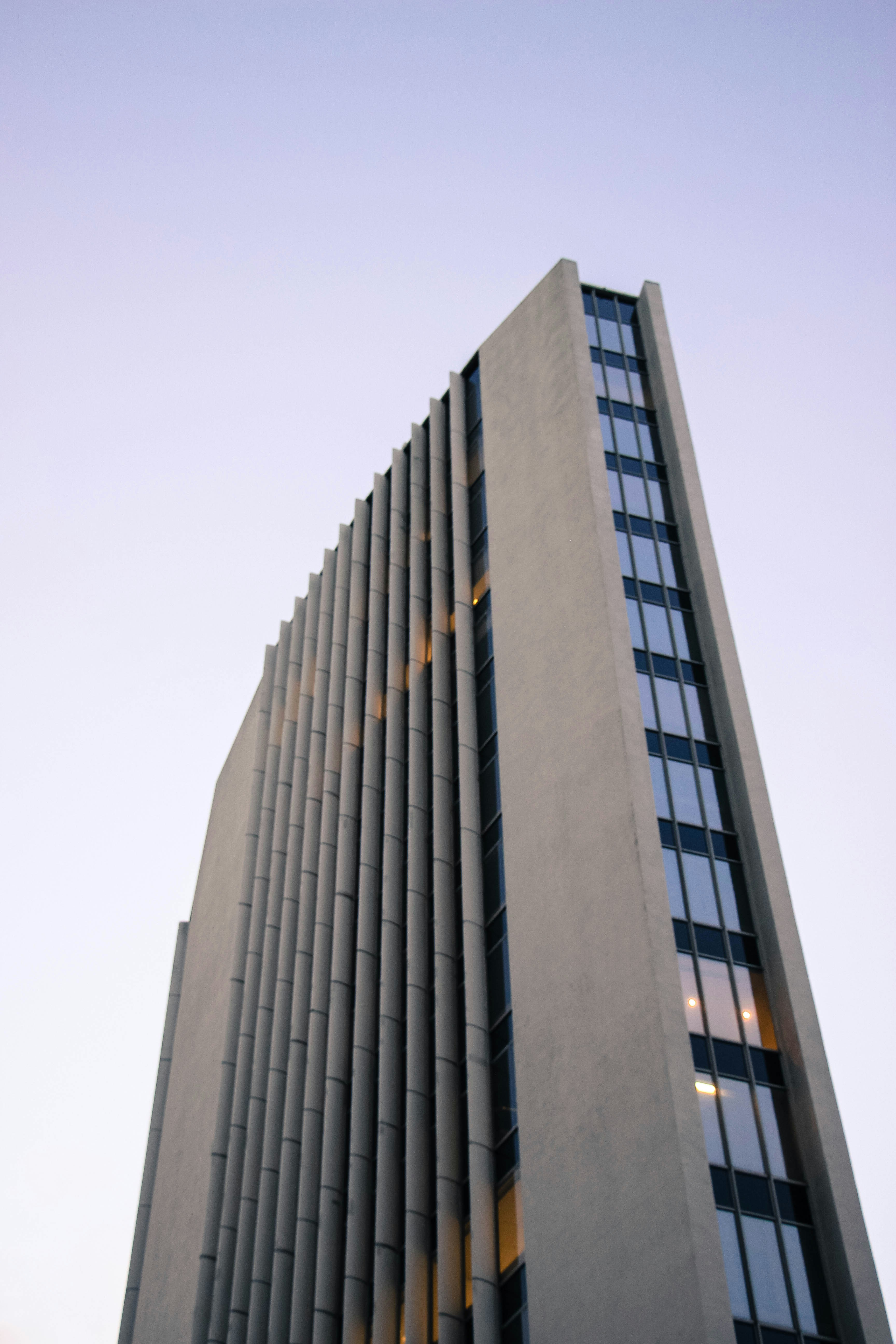 Modern architectural structure with vertical elements and large glass windows, set against a pastel sky at dusk.