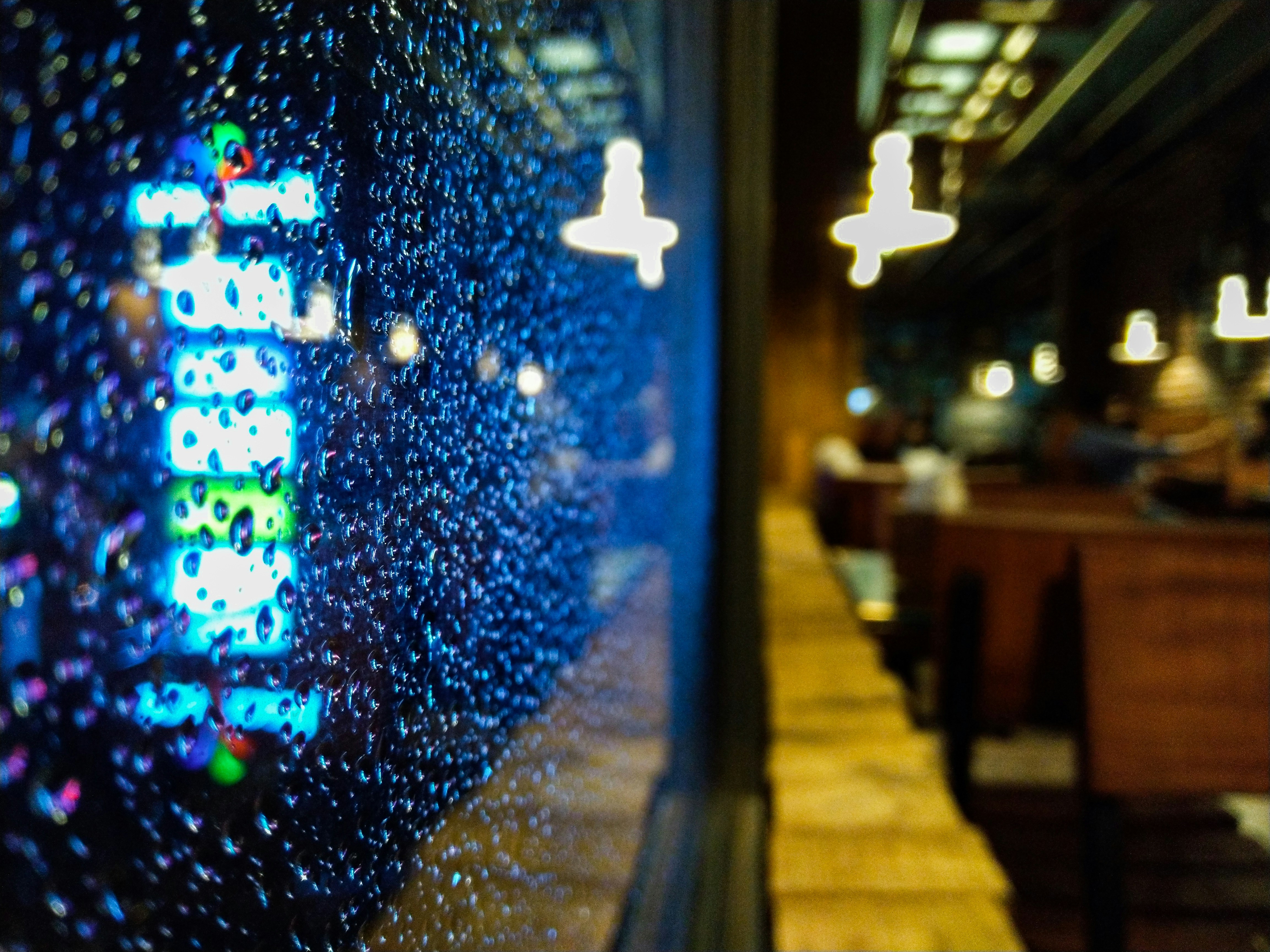 Raindrops on a window reflecting neon lights, with a warm café interior in the background.