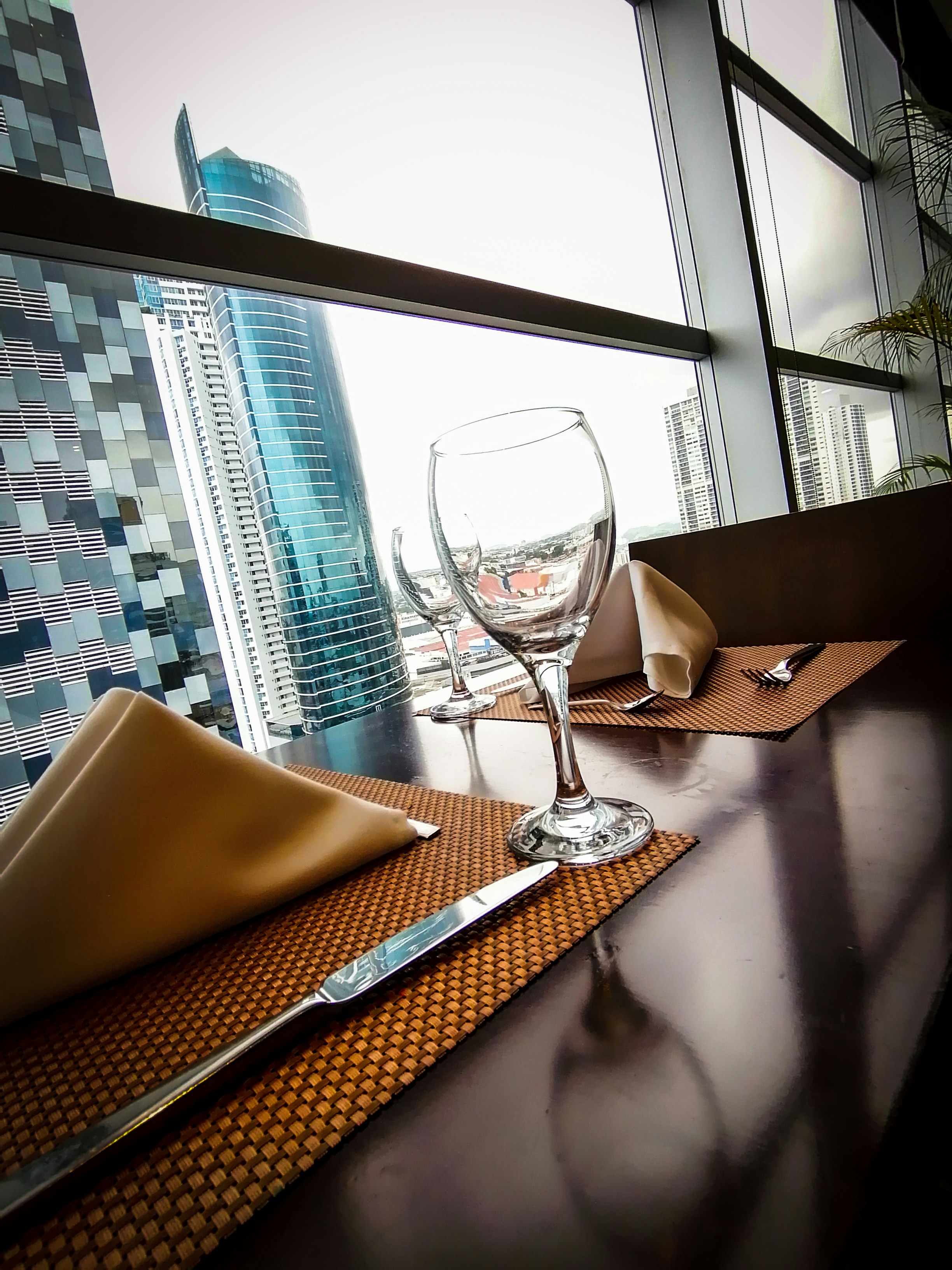 Elegant table setting with a wine glass overlooking a modern cityscape through large windows.