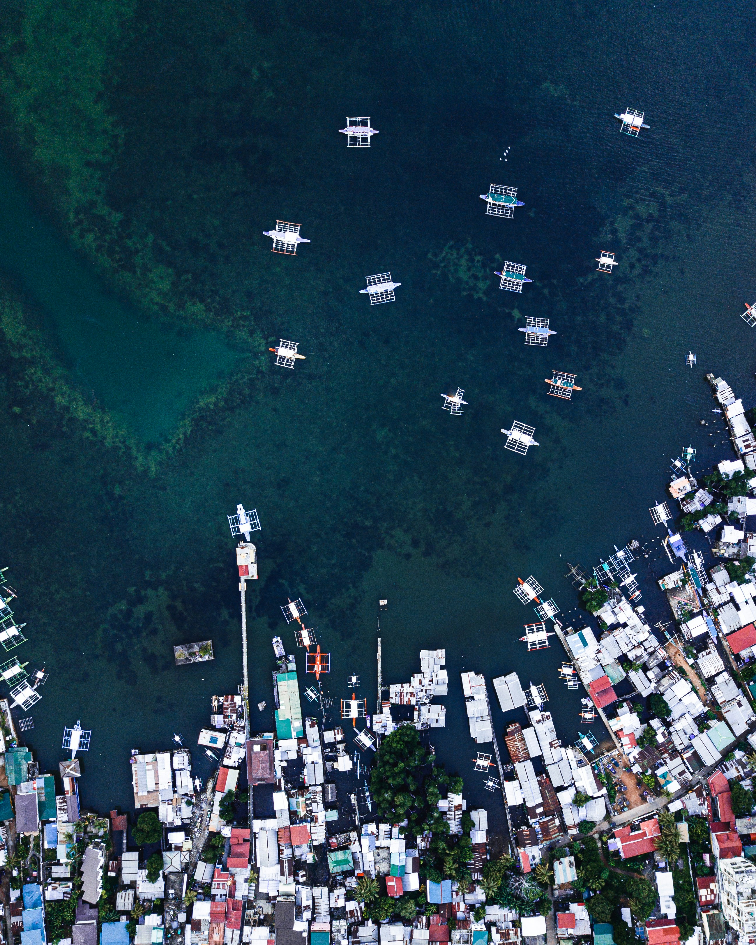 Aerial view showcasing a vibrant coastal settlement with traditional fishing boats scattered across the turquoise waters. The contrast between the colorful rooftops and the serene sea creates a unique landscape.