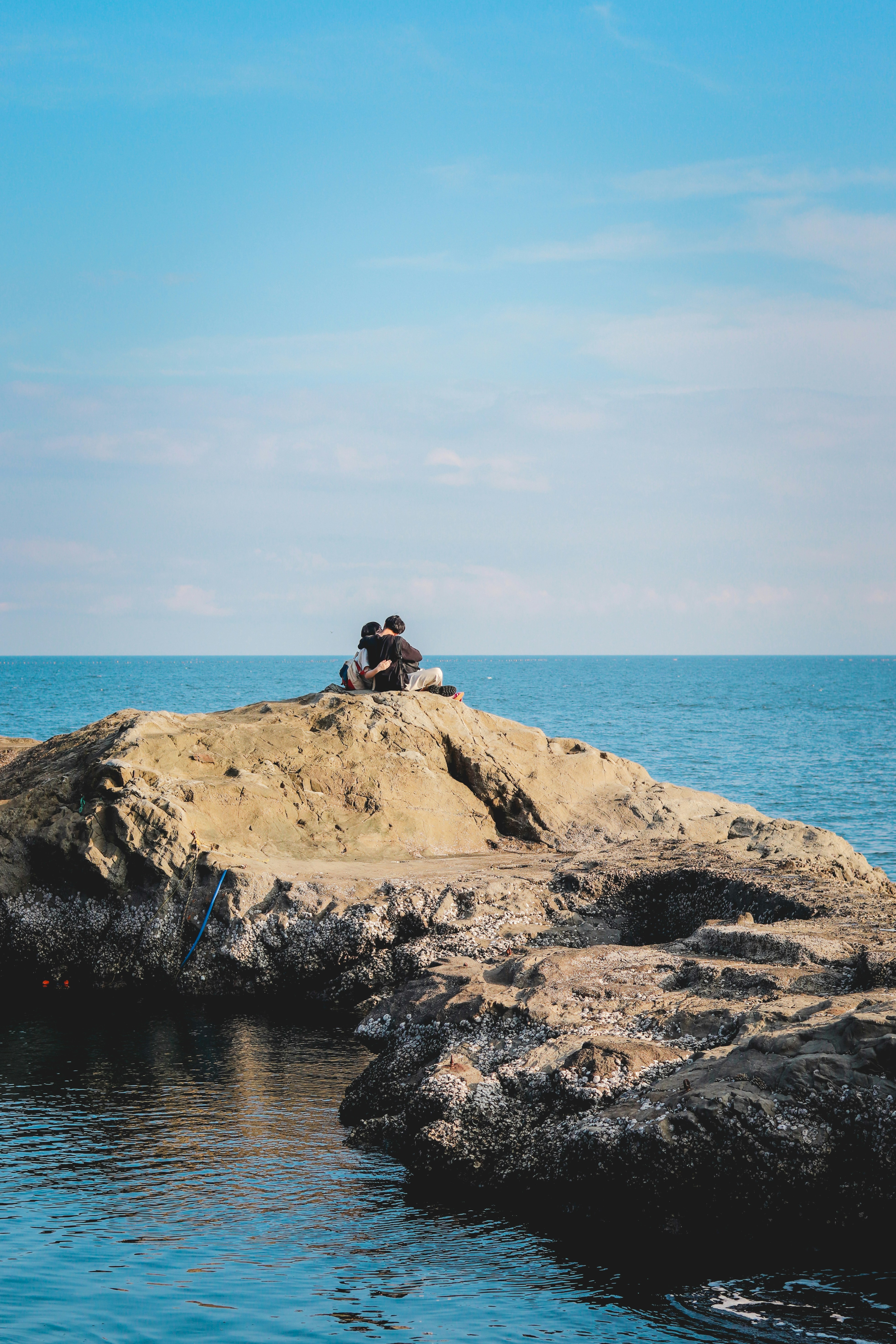 Man sitting on stone beside sea under clear blue sky photo – Free Blue ...