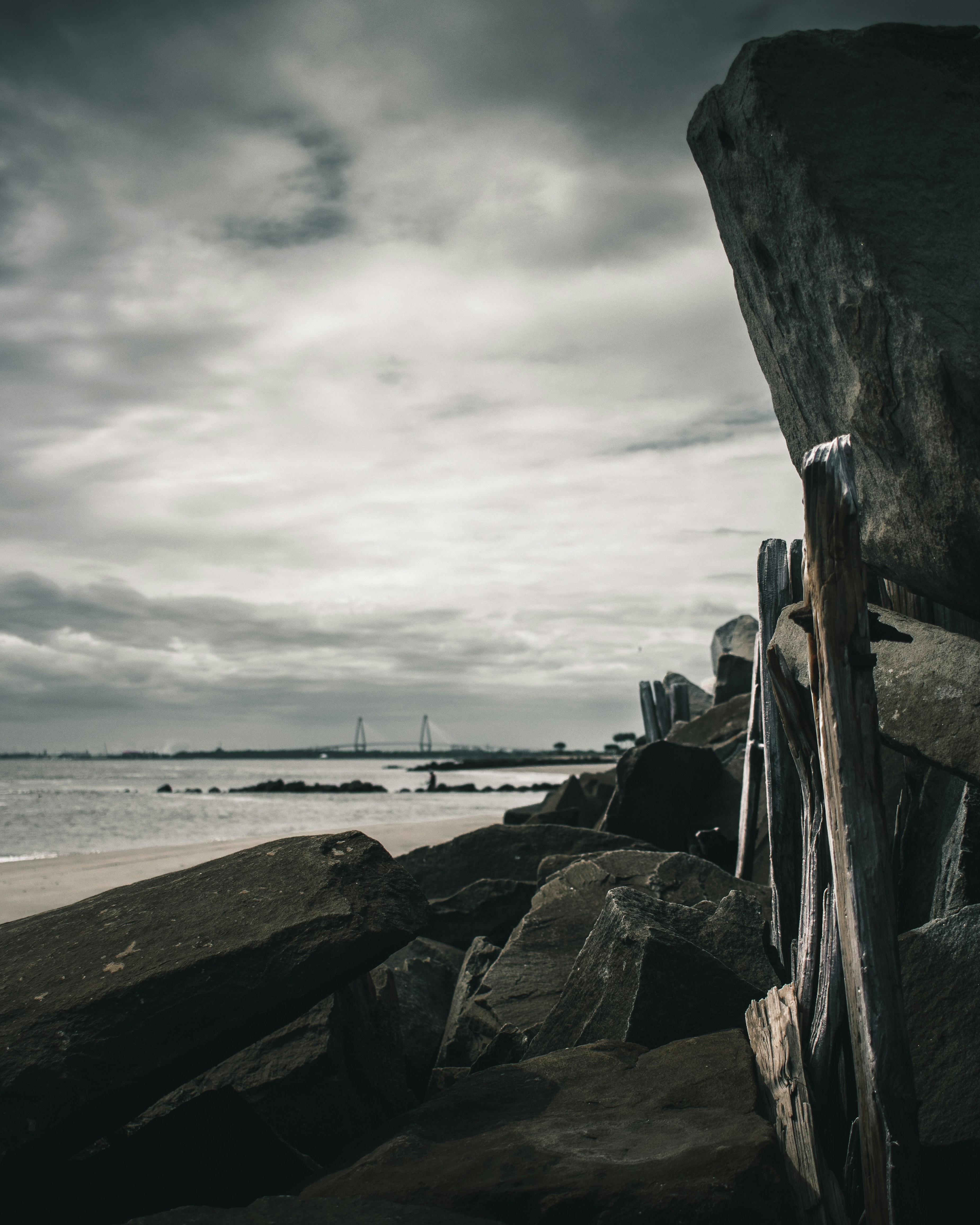 Weathered Groynes Framing a Distant Bridge Under a Moody Coastline