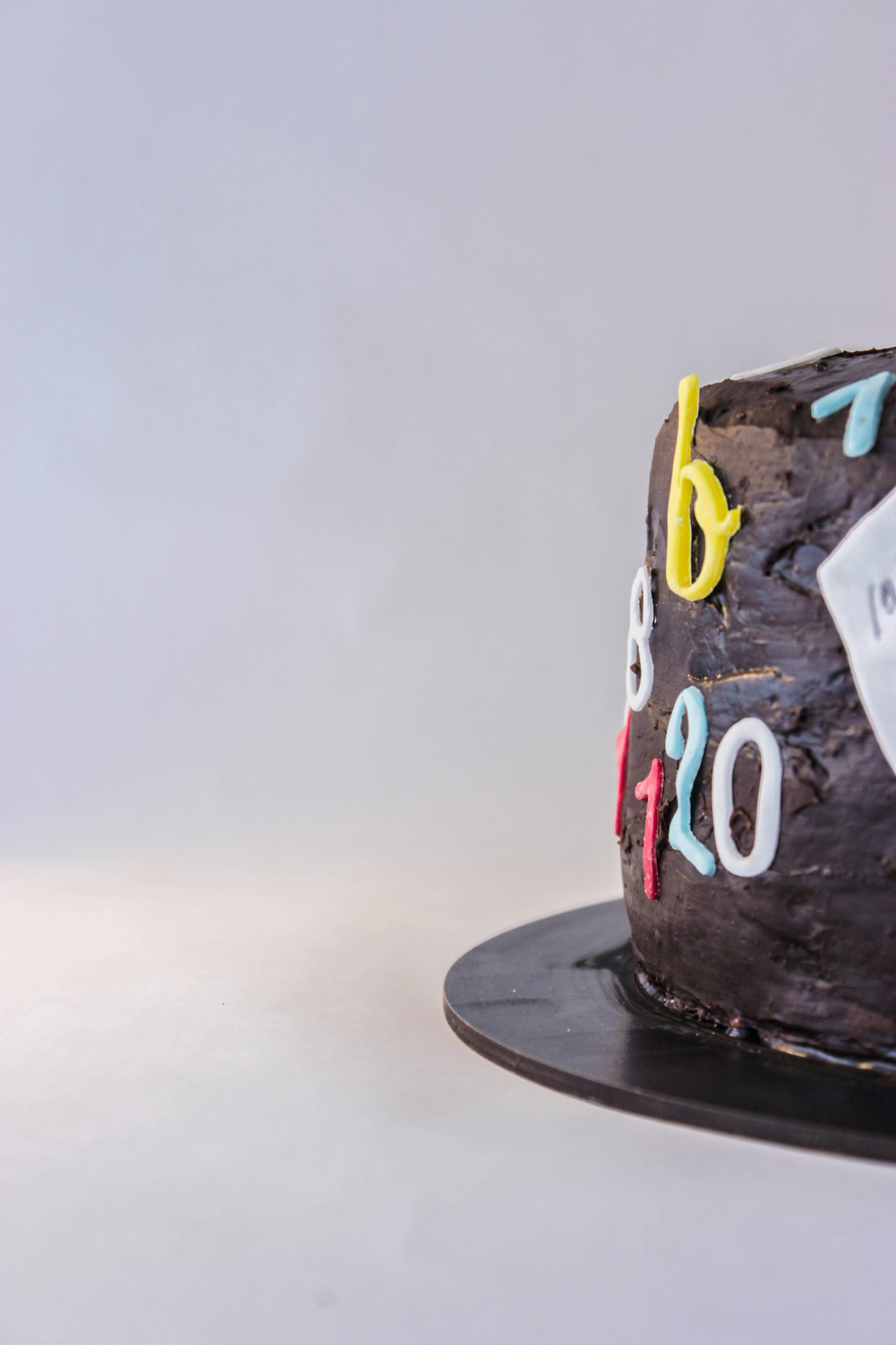 Chocolate cake with colorful numbers decorates a dark icing on a cake board, positioned on the right side of the frame against a pale background.