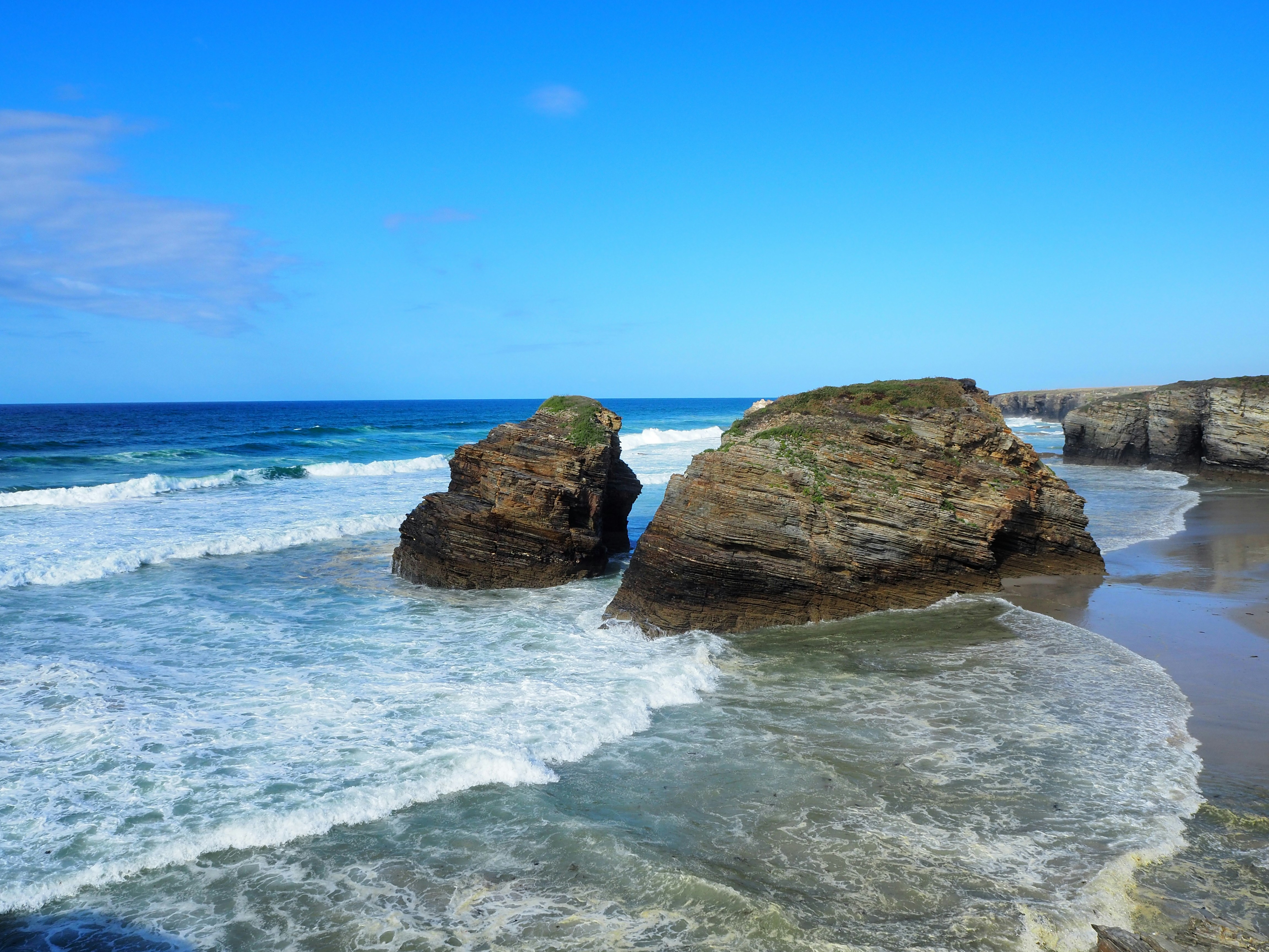 Ocean waves crashing against rugged rock formations under a vibrant blue sky.