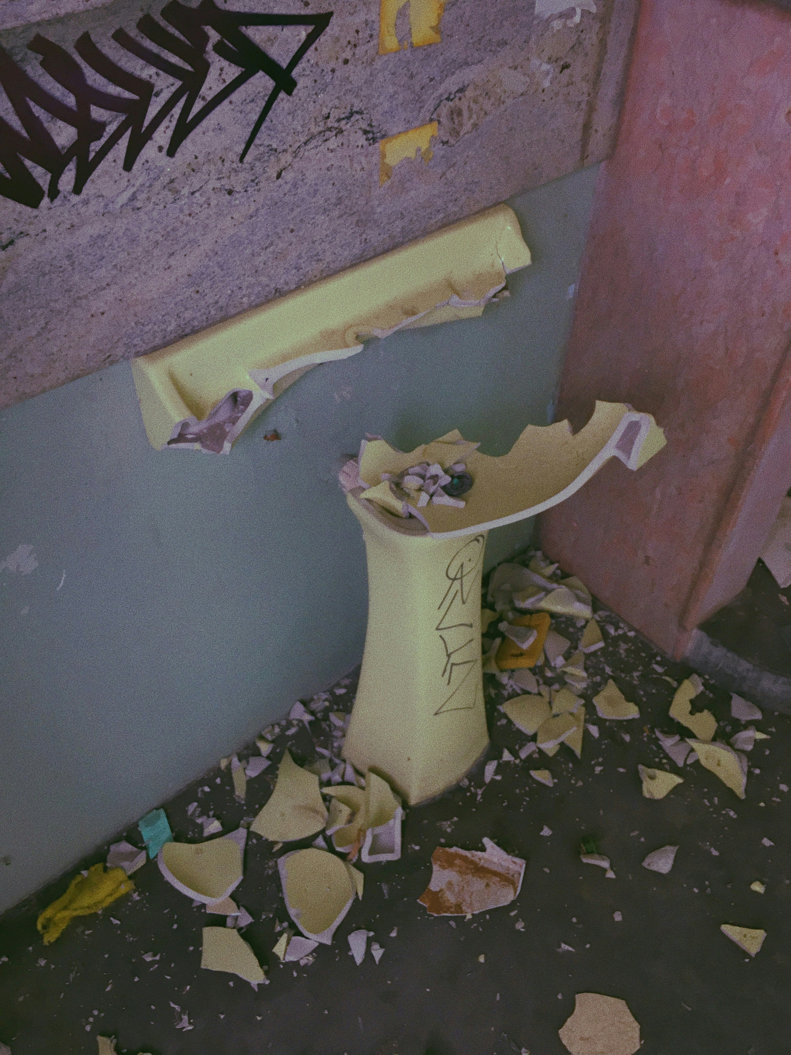 A broken yellow pedestal sits amidst scattered debris and peeling paint, hinting at a once vibrant environment. Graffiti adorns the wall above, adding an urban edge.