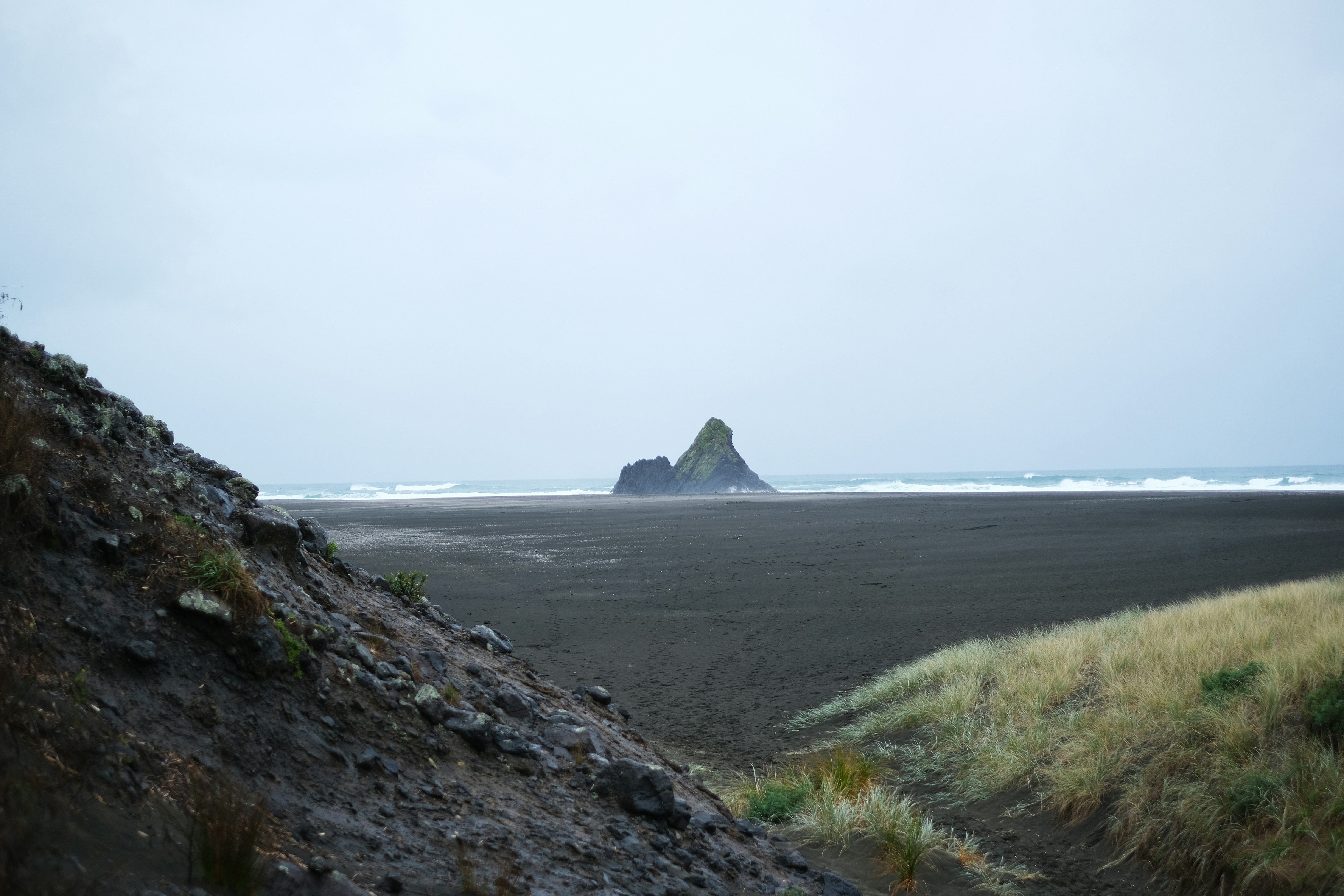 Pinnacle of Quiet: Lone Rock Emerges from a Misty Black-Sand Shore