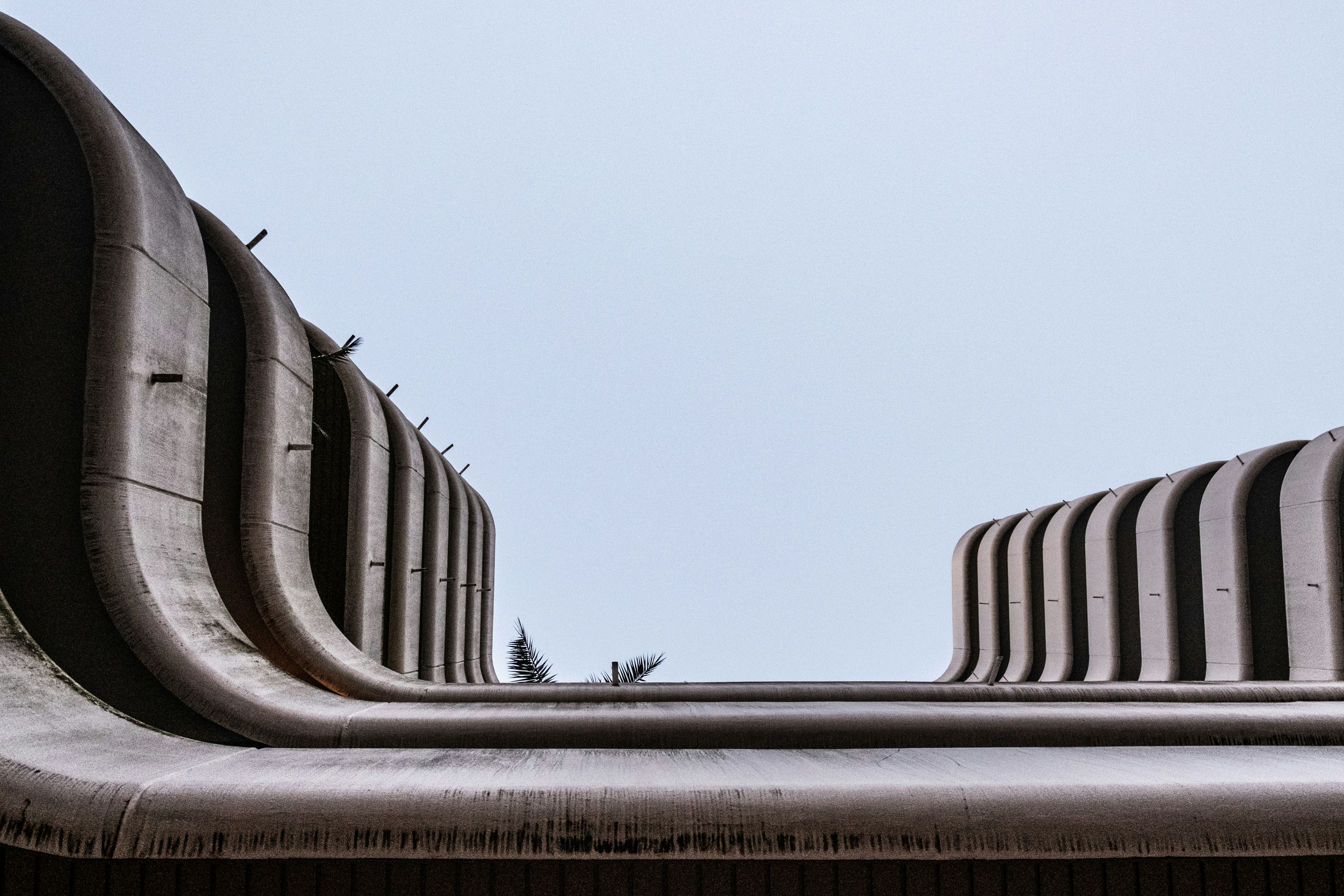 Curved concrete structures create a dynamic visual rhythm against a muted sky, emphasizing architectural design. The image highlights the interplay of lines and shapes.