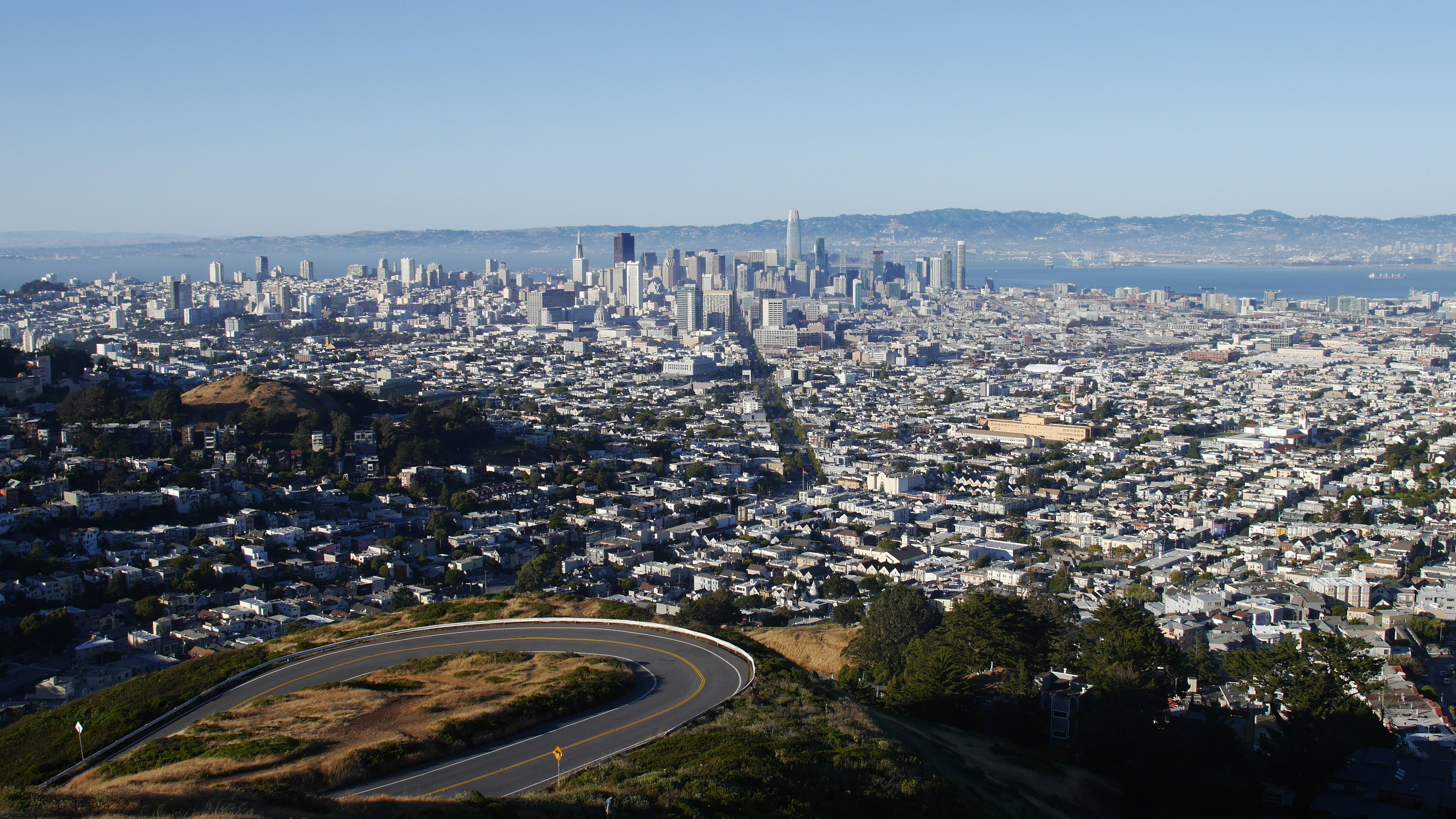 Panoramic view of a sprawling cityscape with winding roads and distant skyscrapers under a clear blue sky.