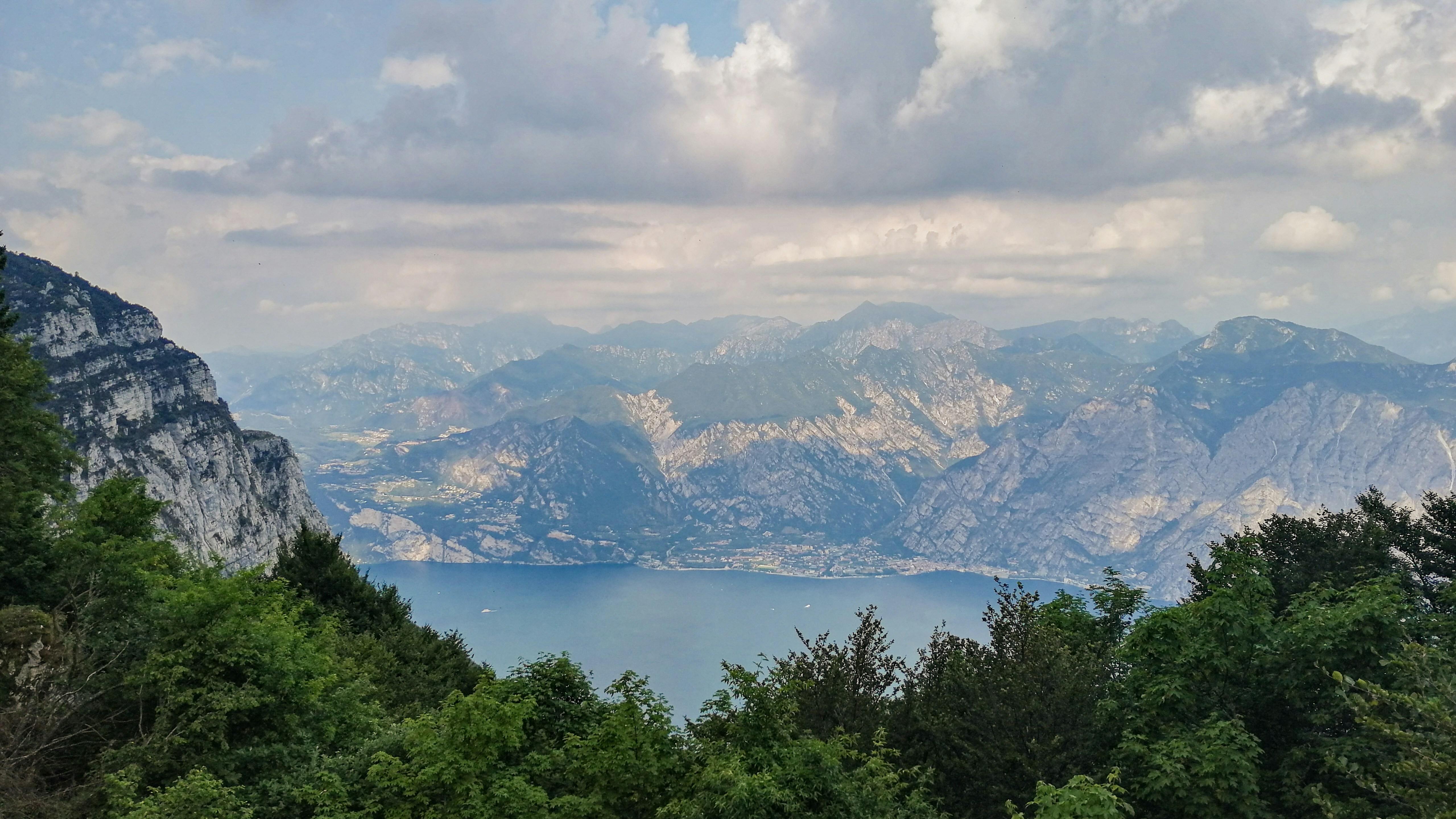 Vast lake reflecting the rugged mountains under a dynamic sky, framed by lush greenery in the foreground.