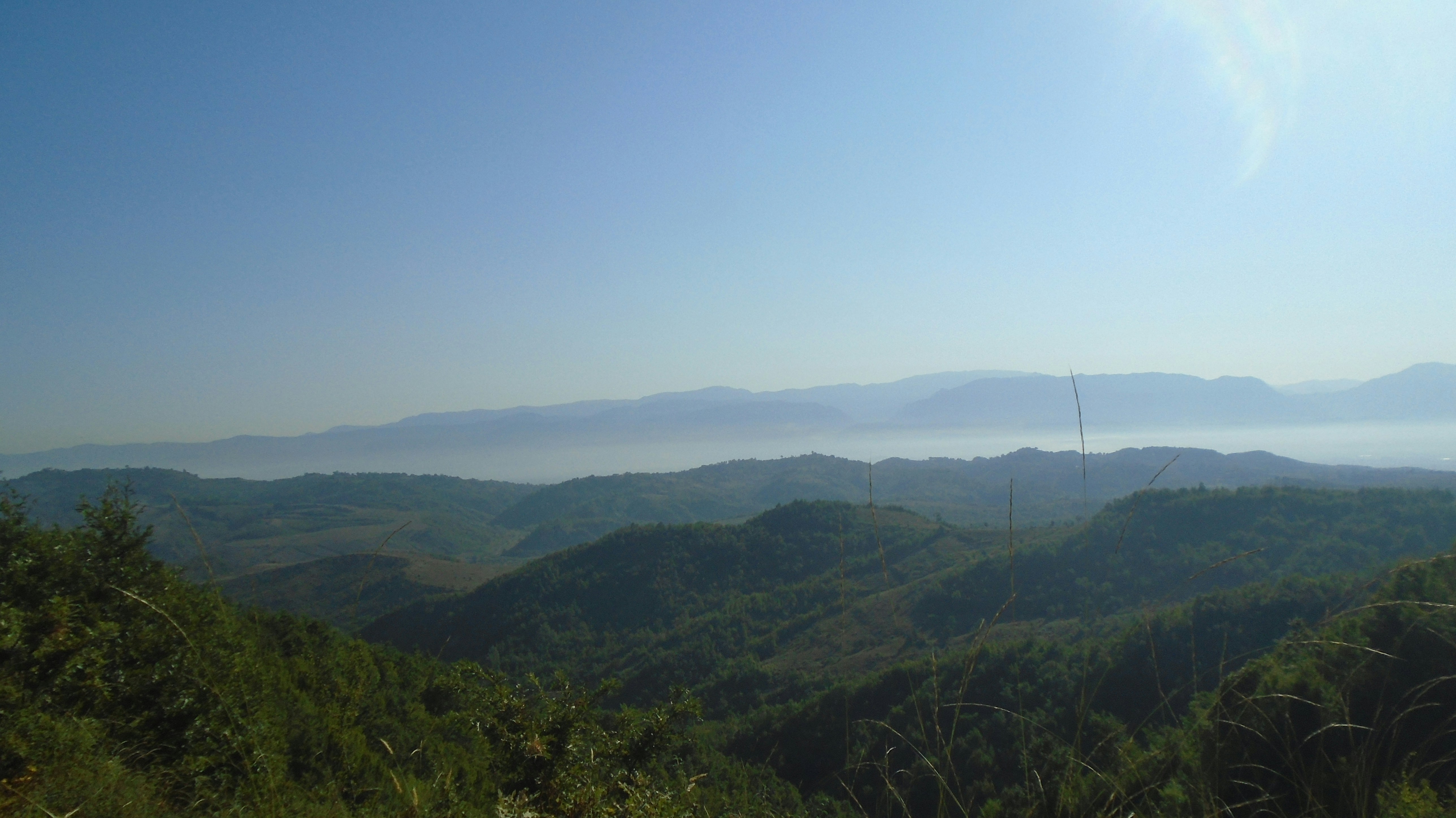 Vast landscape of rolling hills under a clear blue sky, showcasing layers of mountains in the distance.