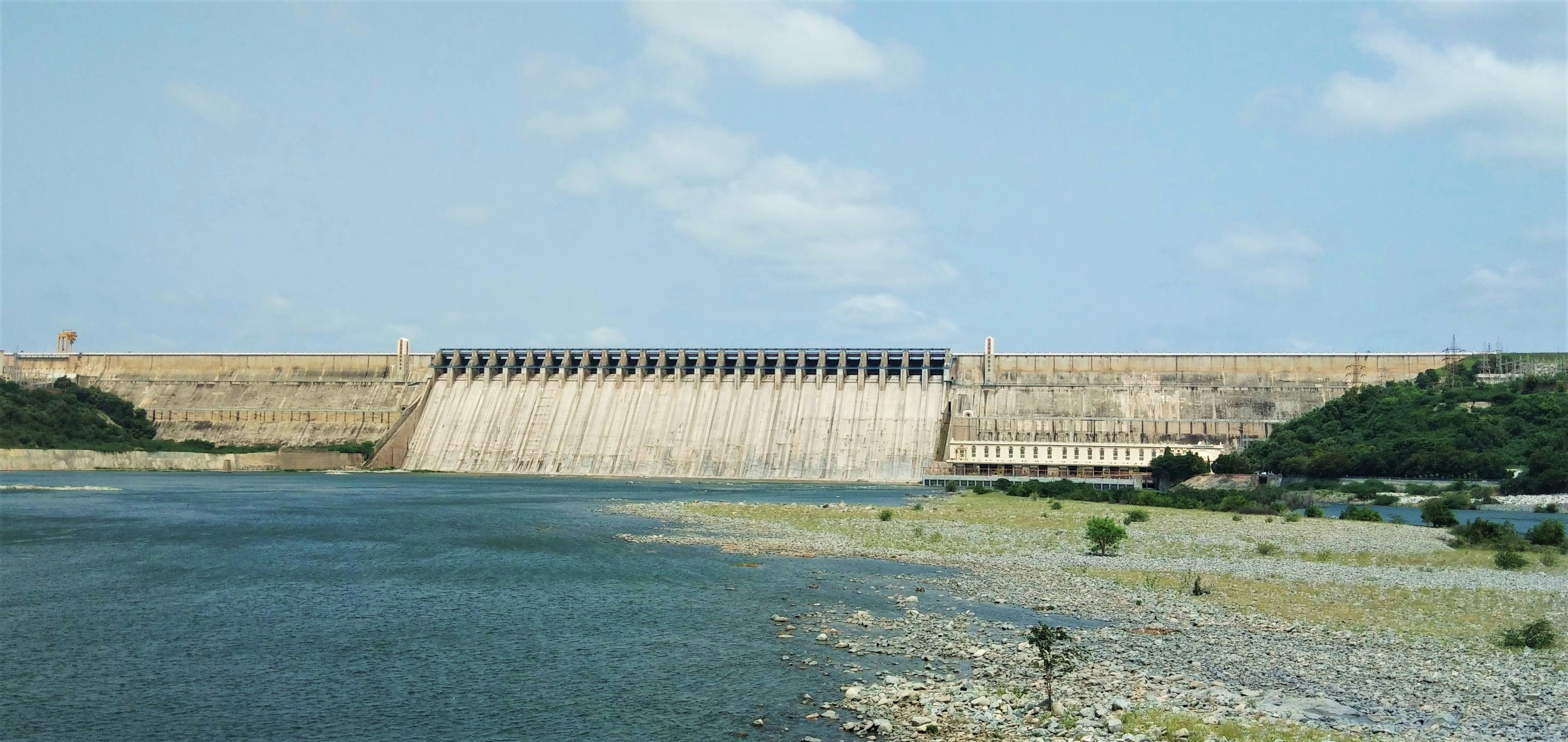 Expansive dam structure with cascading water set against a clear blue sky.