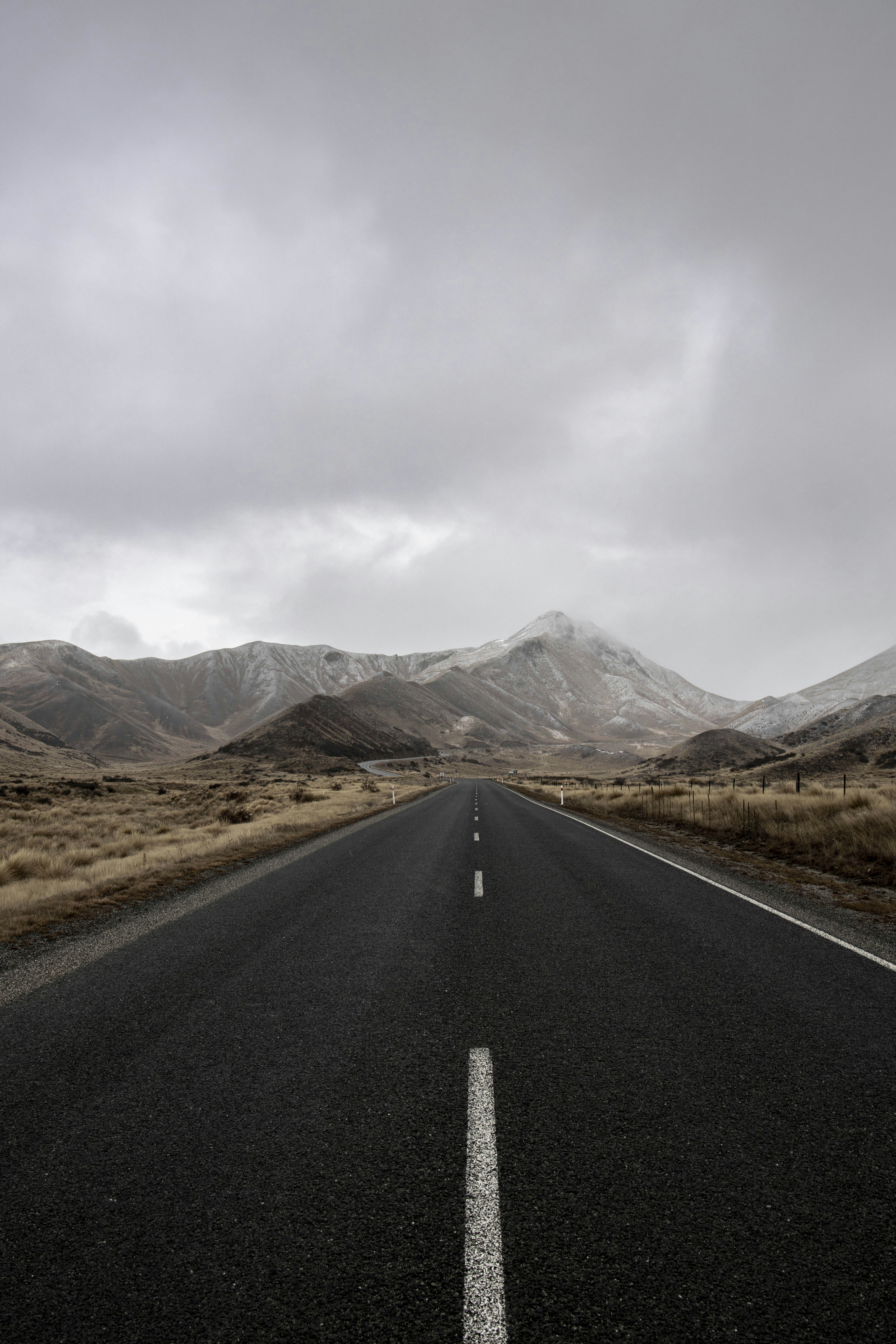 Lonely road stretching toward distant mountains under a moody sky, evoking a sense of adventure and solitude.