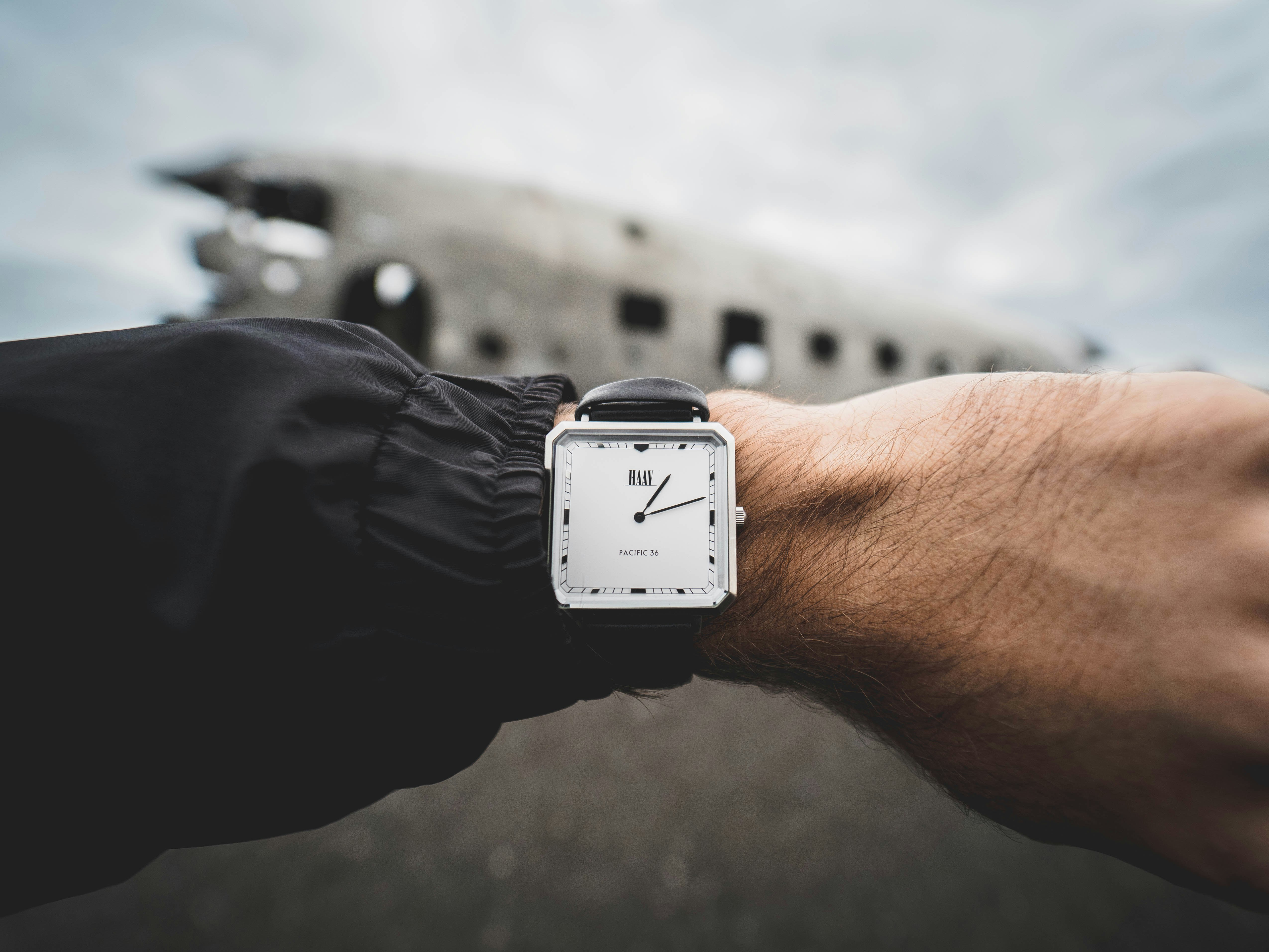 Square Dial, Soft Horizon: A Wristwatch Framed by a Distant Steel Vessel