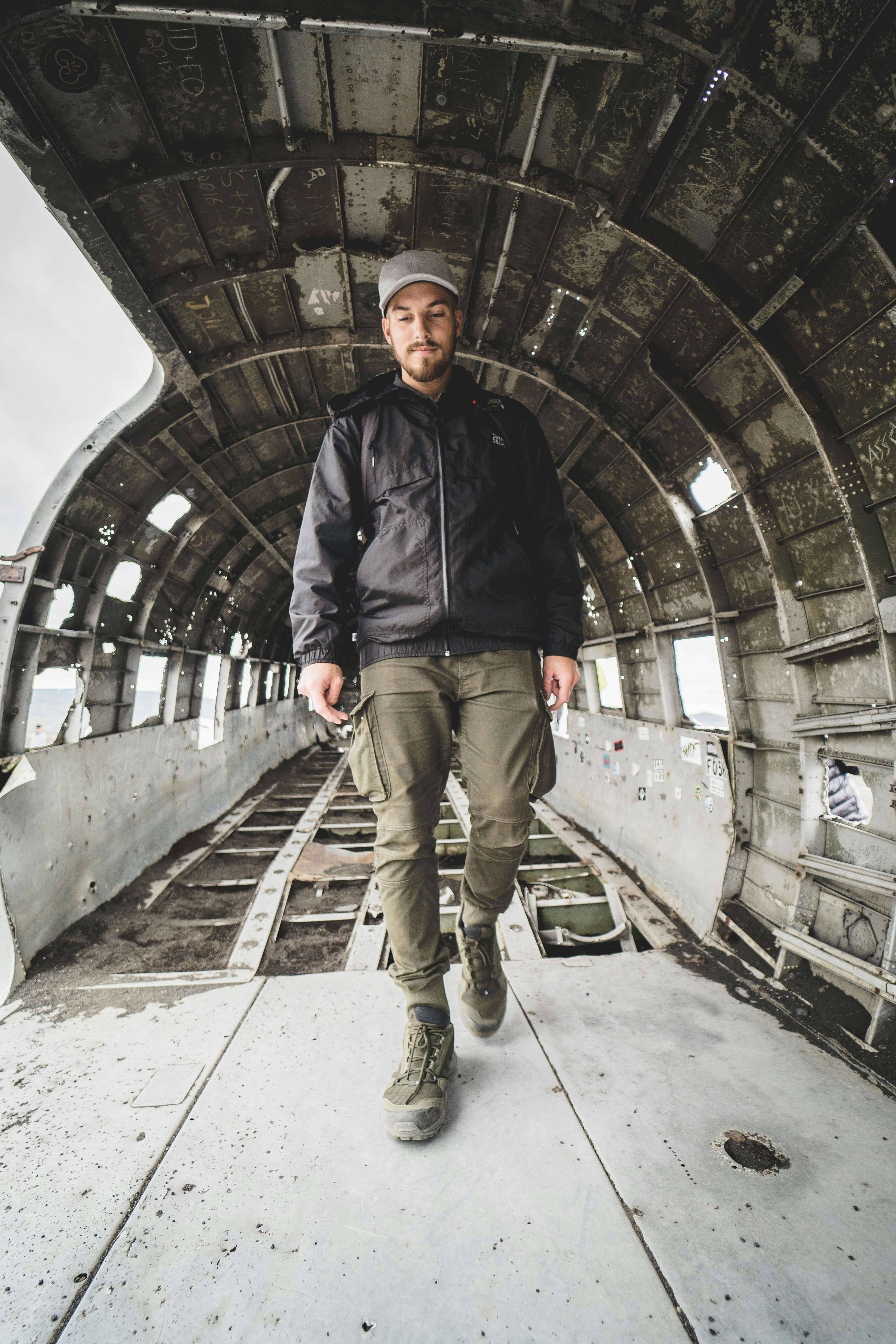 A person walks inside the decaying interior of an abandoned aircraft, surrounded by weathered metal and remnants of its past.
