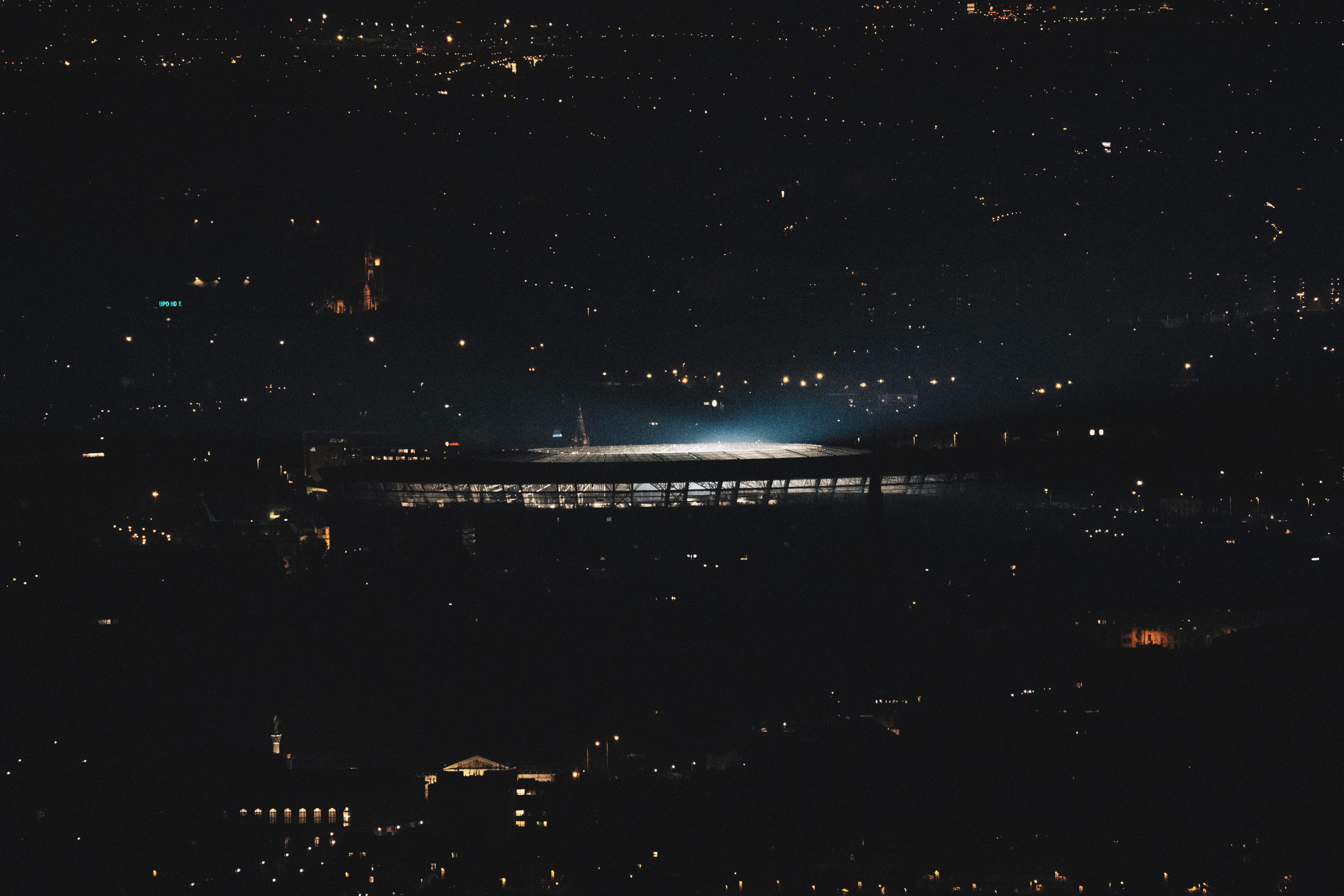 A stadium illuminated in the distance, surrounded by a sea of city lights under a dark sky.