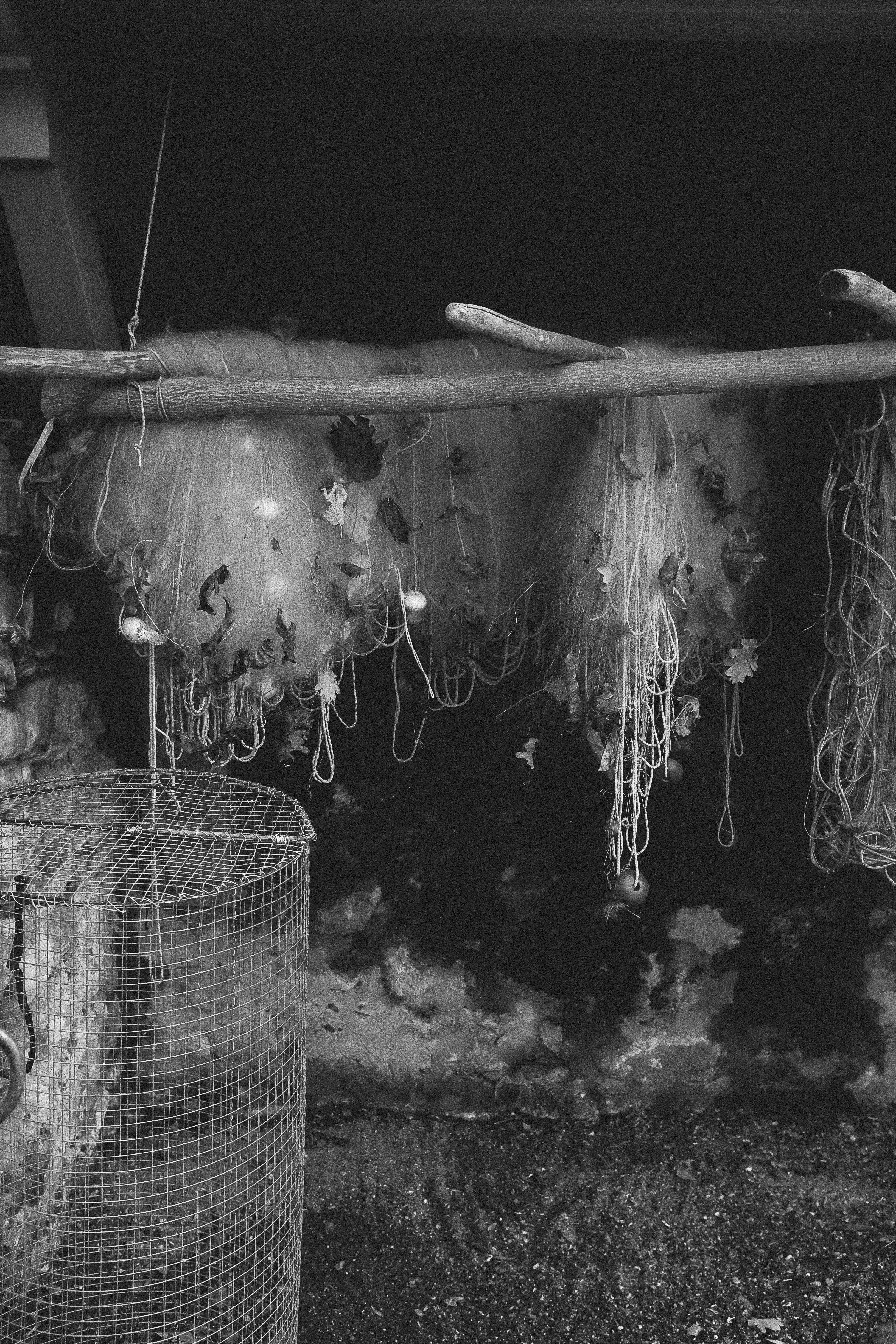 Delicate fishing nets suspended against a textured wall, showcasing the interplay of light and shadow. A wire basket rests nearby, hinting at the fishing heritage.