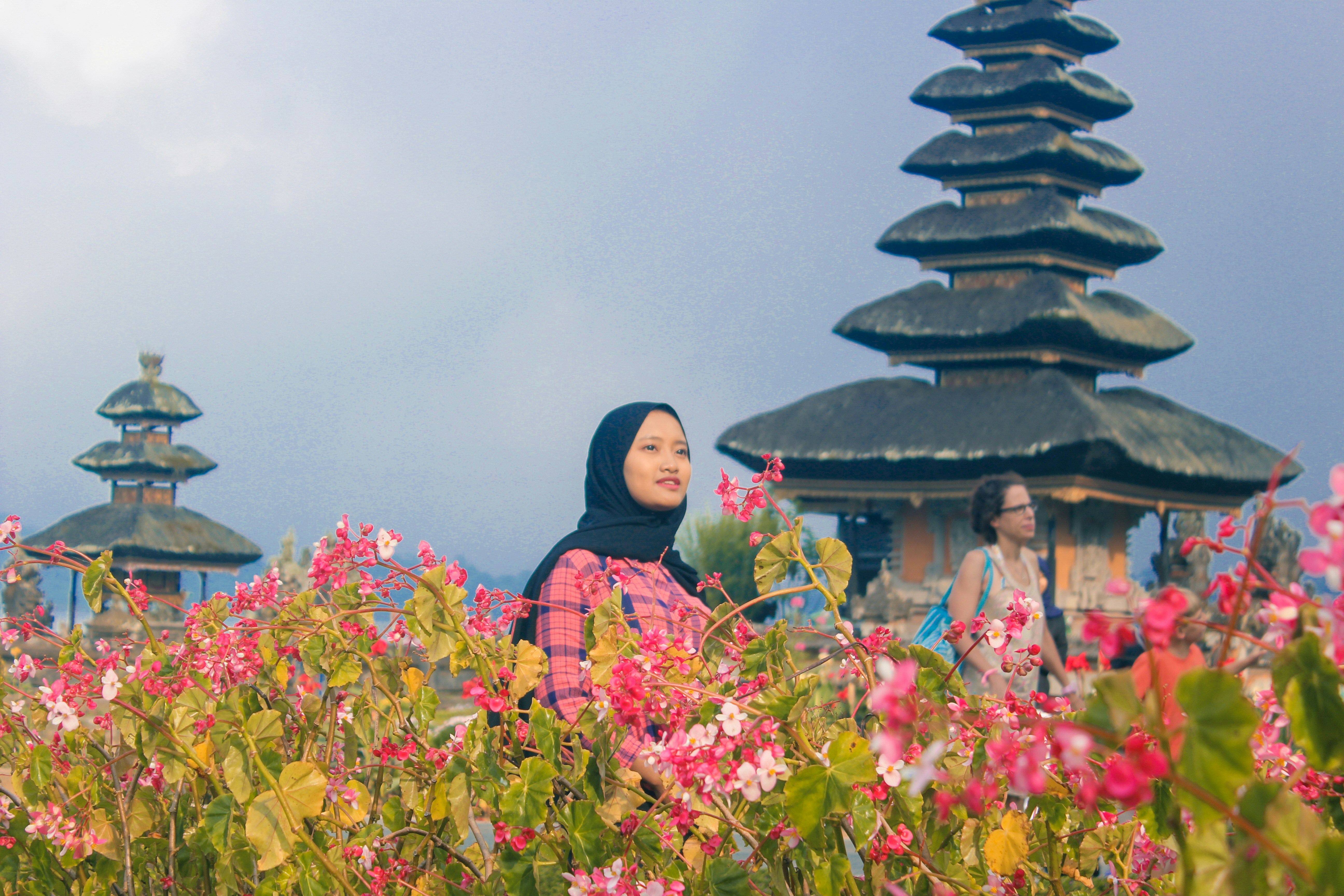 Portrait Through a Pink Sea: A Hijab-Clad Figure Framed by Flower Foreground and Pagoda Towers