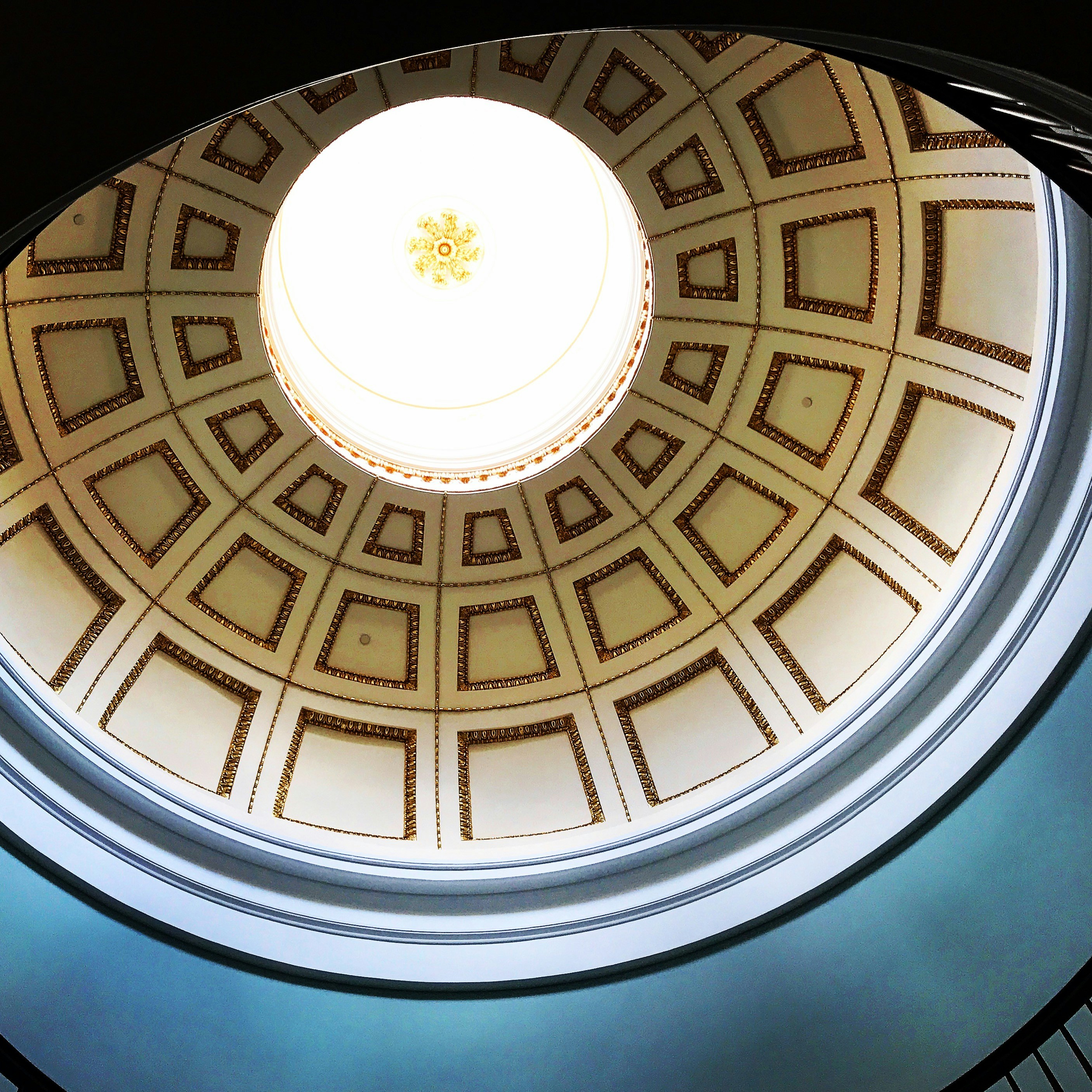 Circular coffered dome ceiling with a central skylight, viewed from below, revealing repeating square recesses and warm illumination.