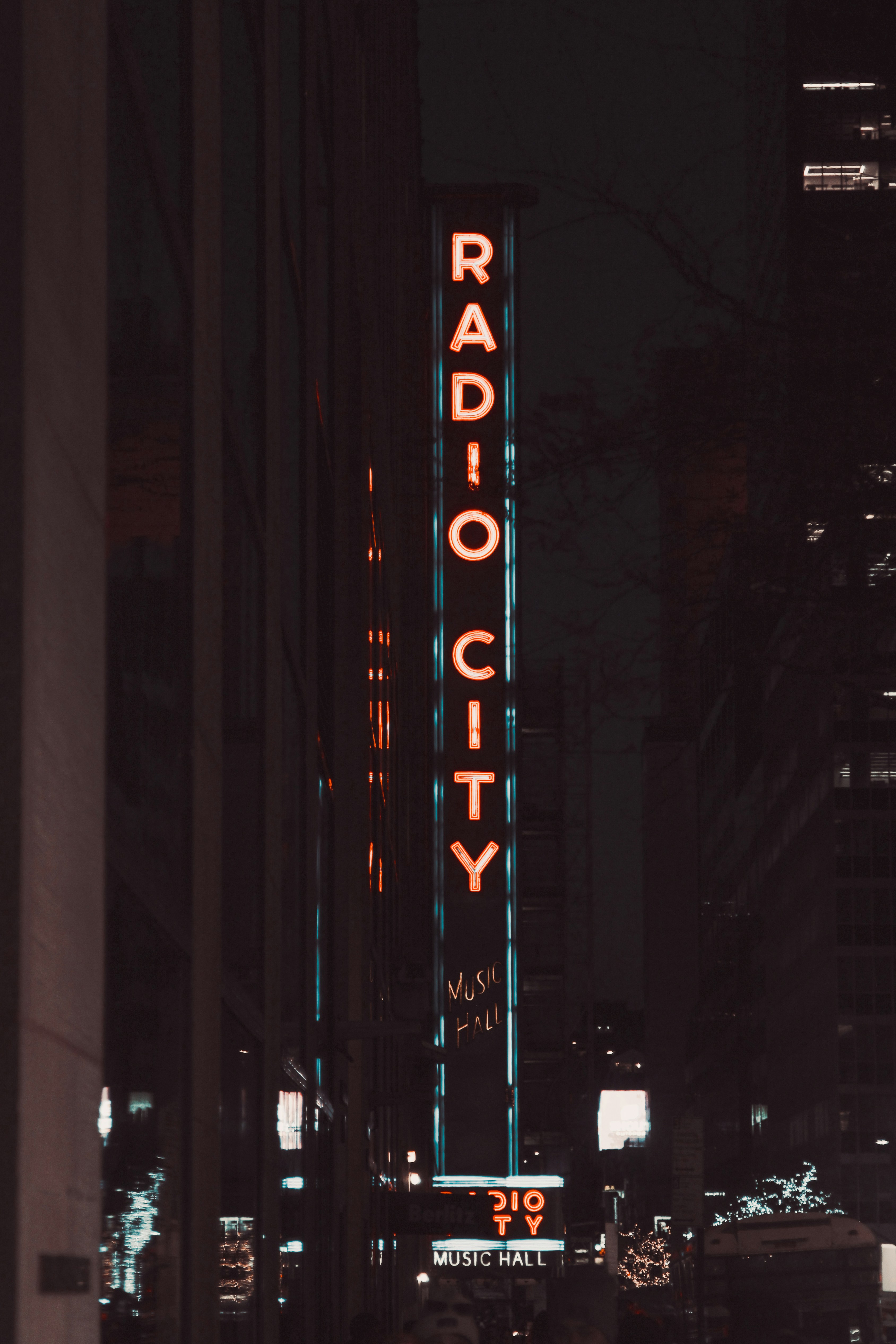 Illuminated RADIO CITY sign against a dark urban backdrop, showcasing its iconic presence. The neon lights reflect the vibrant energy of the city.