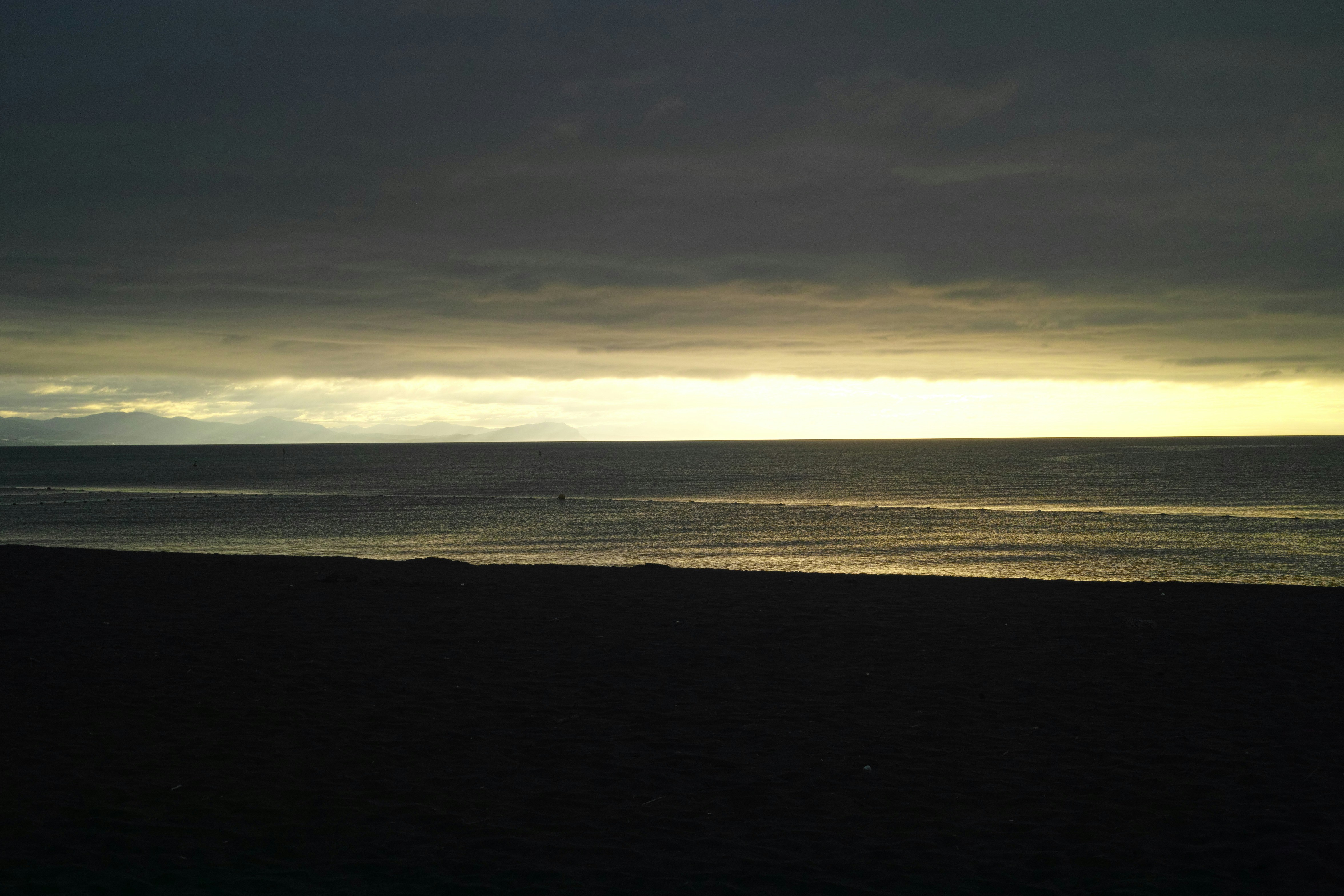 Calm sea under a cloudy sky with a soft yellow glow on the horizon.