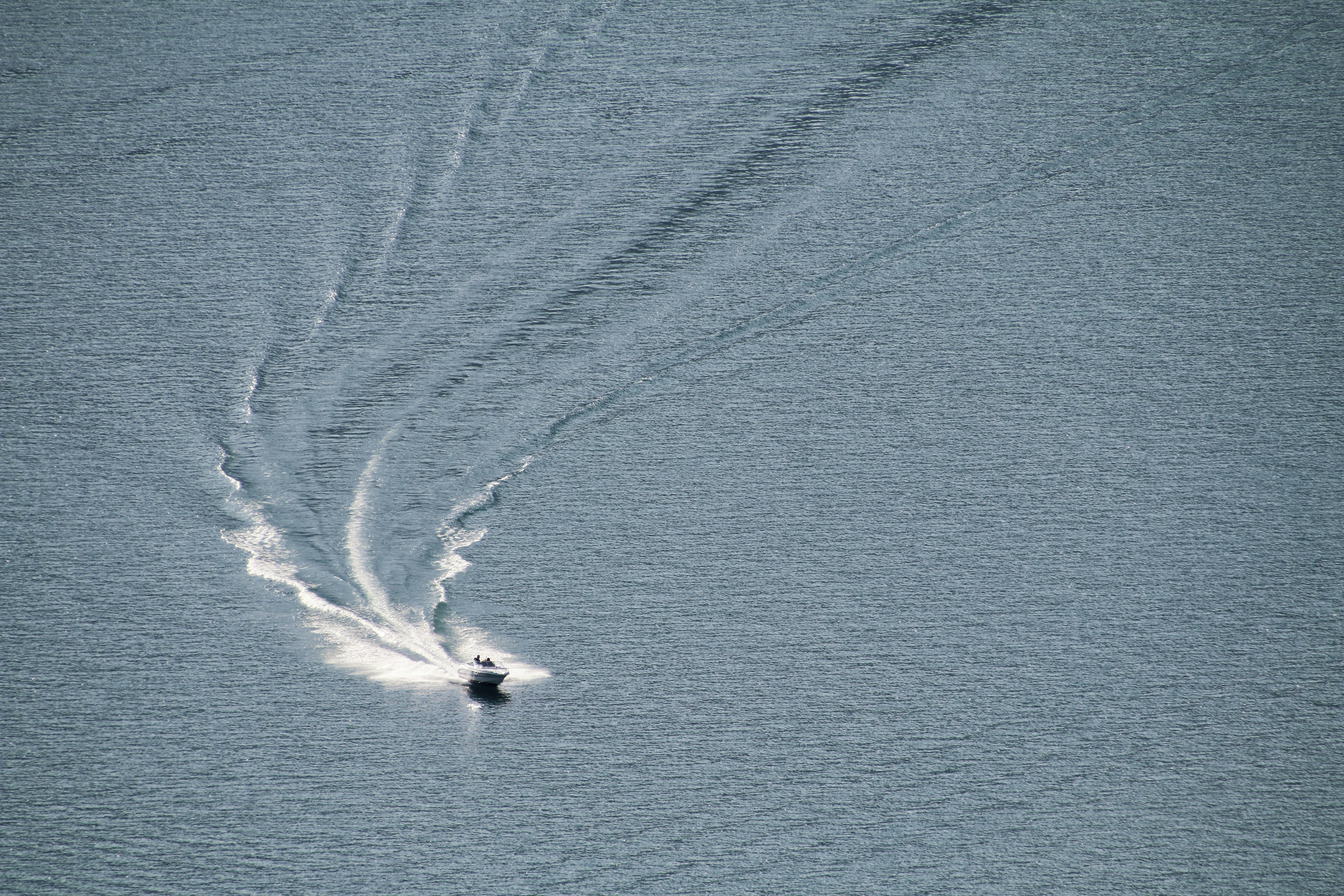 Twin wake arcs: a solitary boat glides through a tranquil blue sea