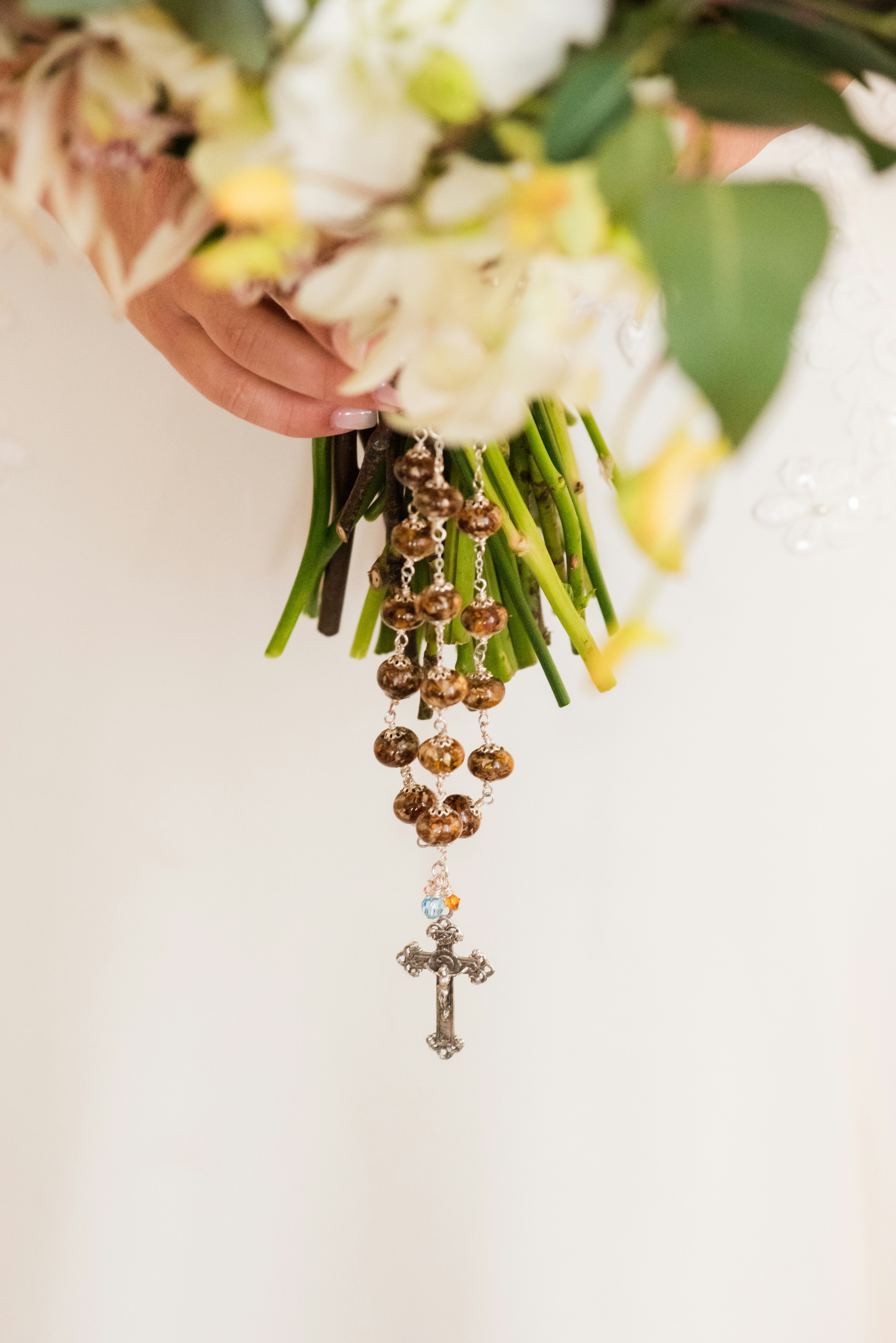 Delicate bouquet adorned with a rosary featuring a cross, held gently in a hand. The arrangement blends natural beauty with spiritual significance.