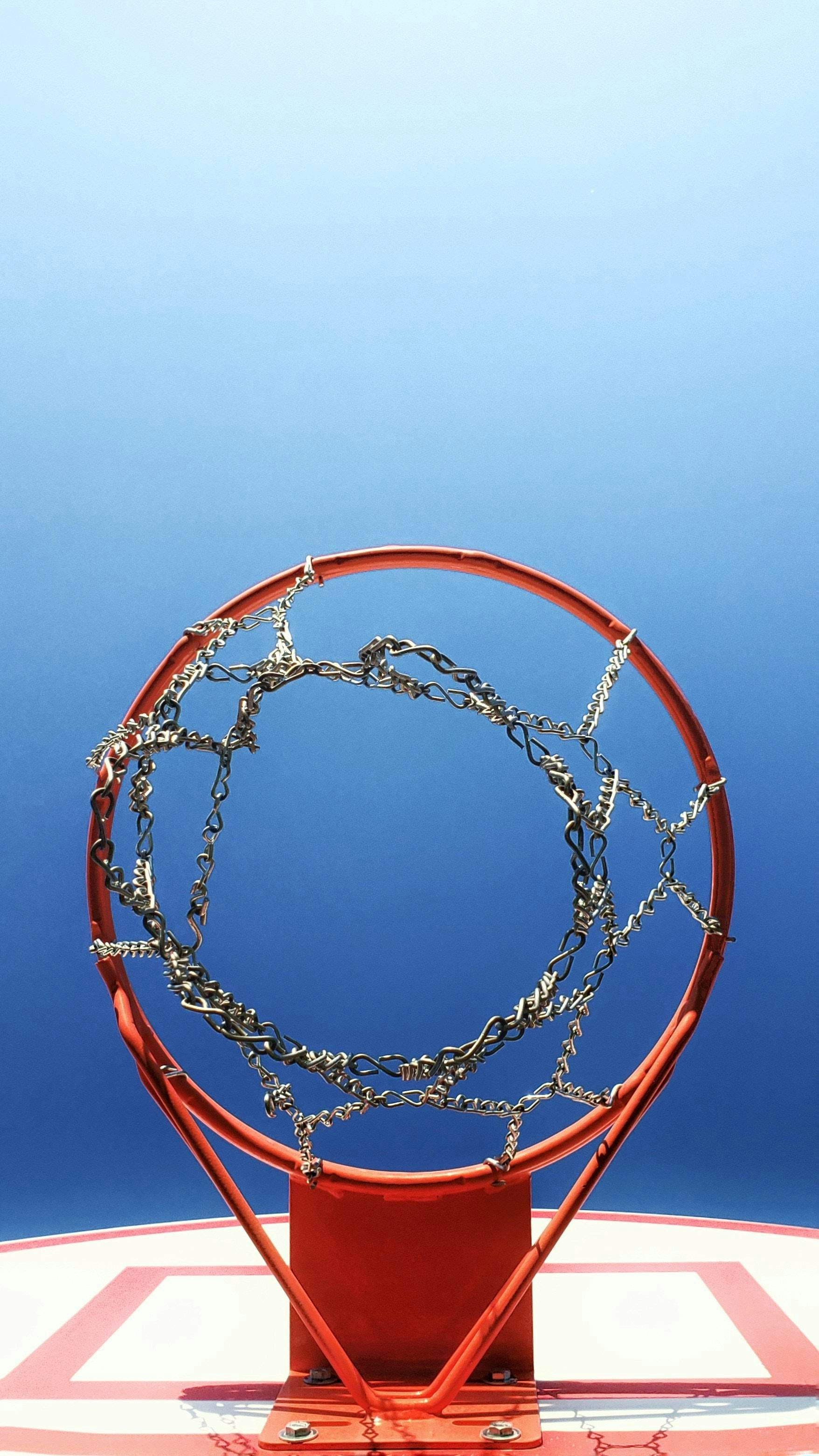 Basketball hoop against a gradient blue background, showcasing the intricate chain net. The simplicity highlights the sport's core elements.