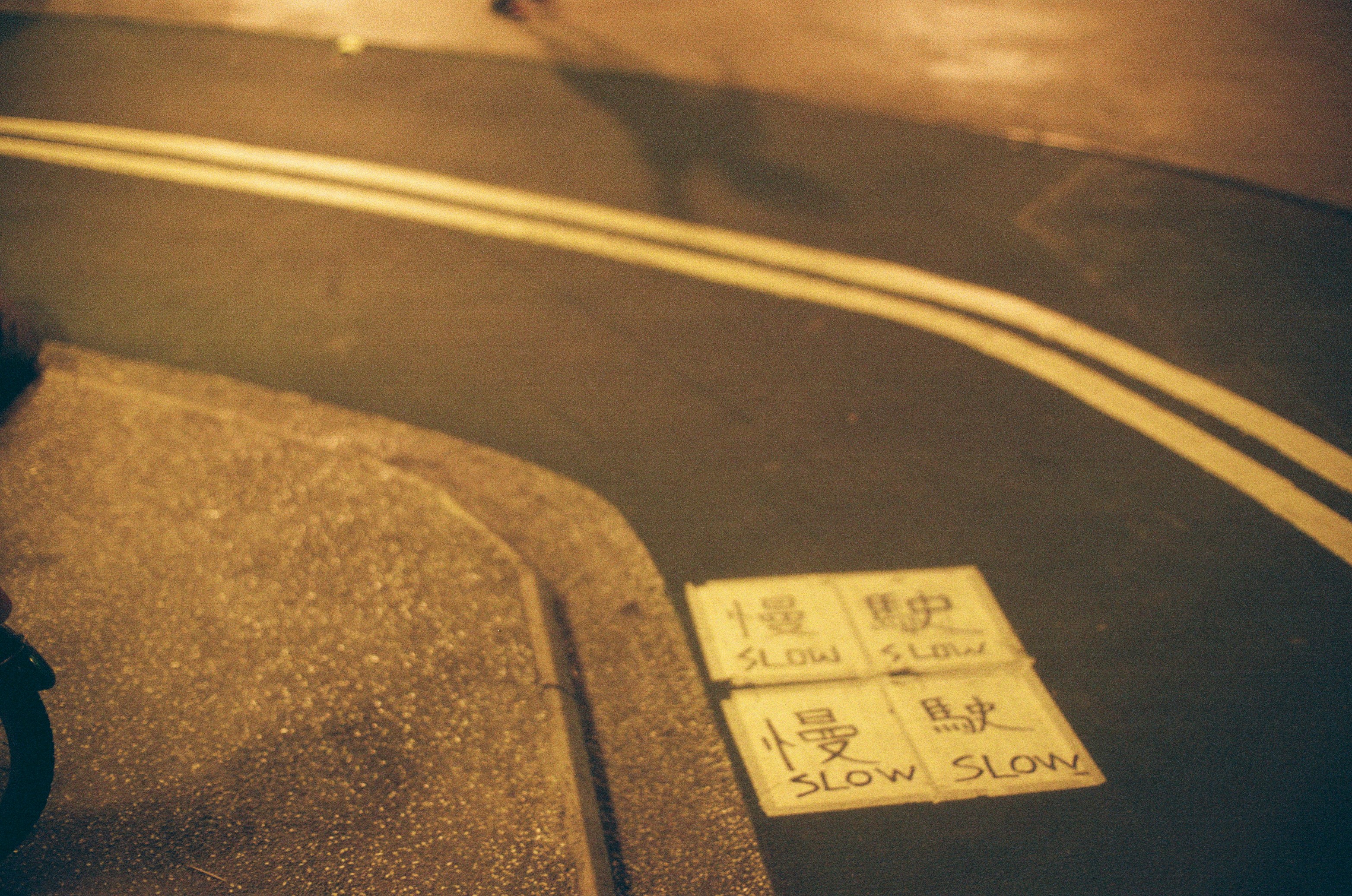 Two square street tiles read SLOW on a weathered curb, illuminated by warm streetlight. A quiet, nighttime urban moment captured up close.