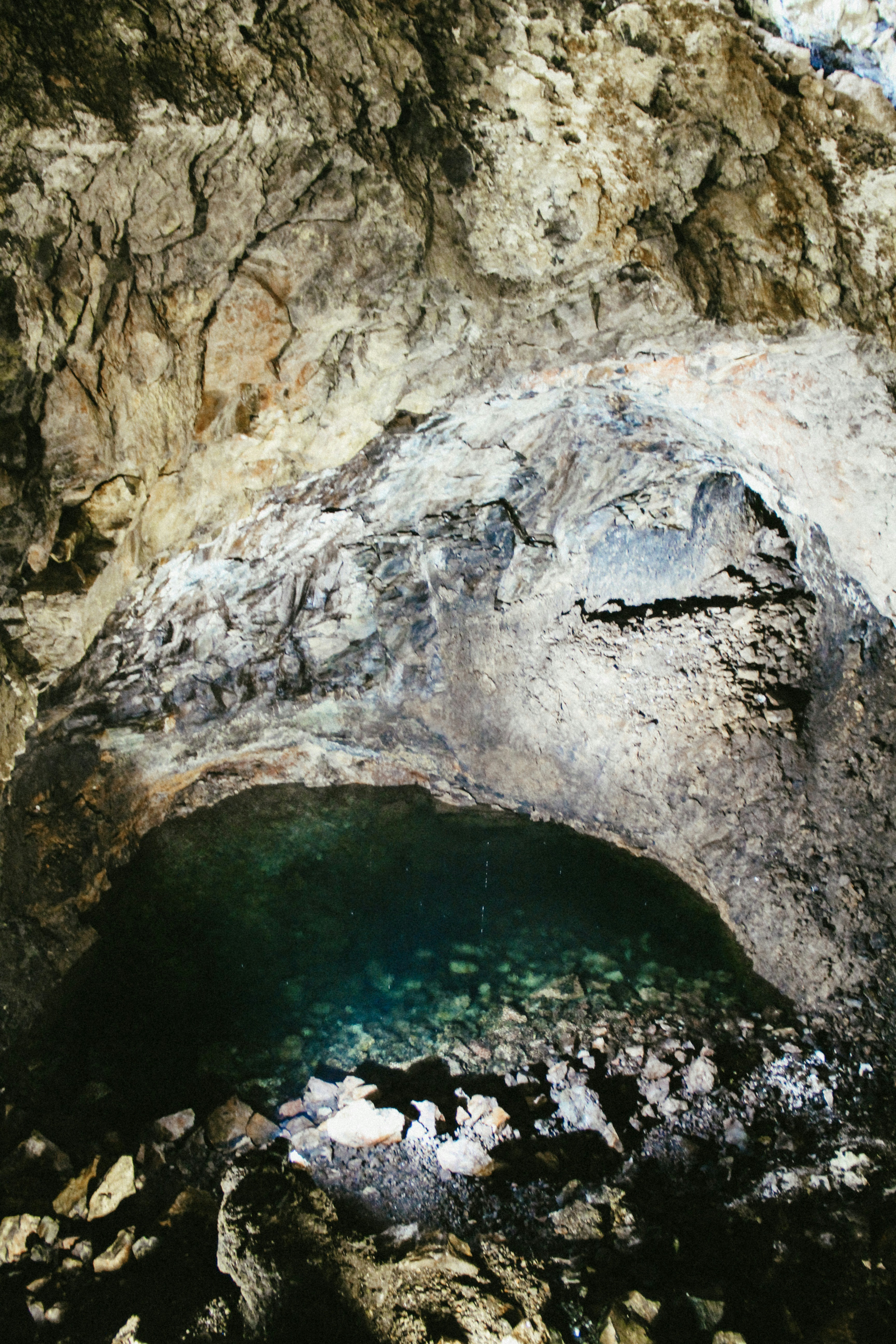 A serene underground pool reflecting the rugged textures of the cave walls, illuminated by soft light filtering from above.