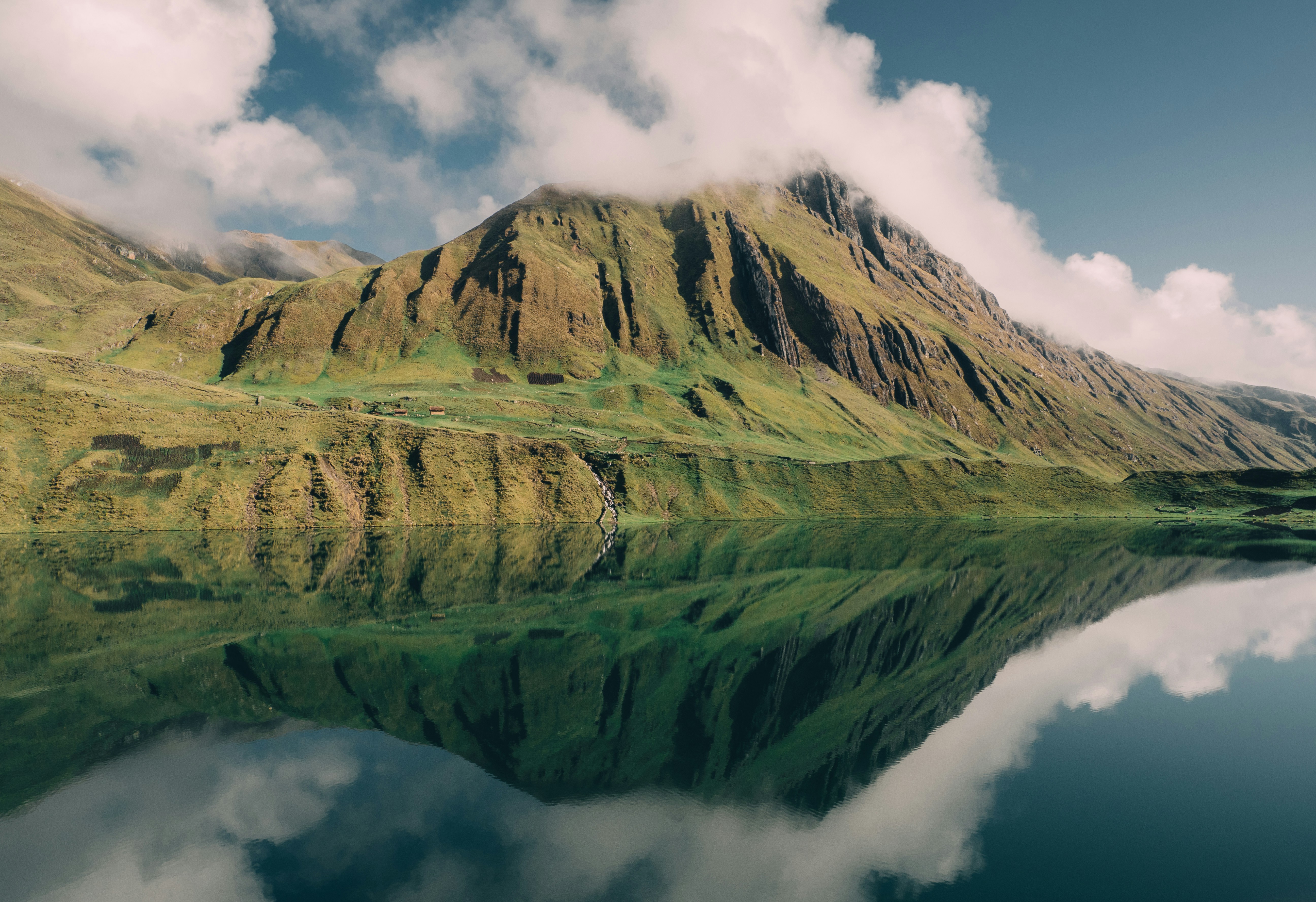 Mountain landscape reflected in a tranquil lake under a sky dotted with clouds.