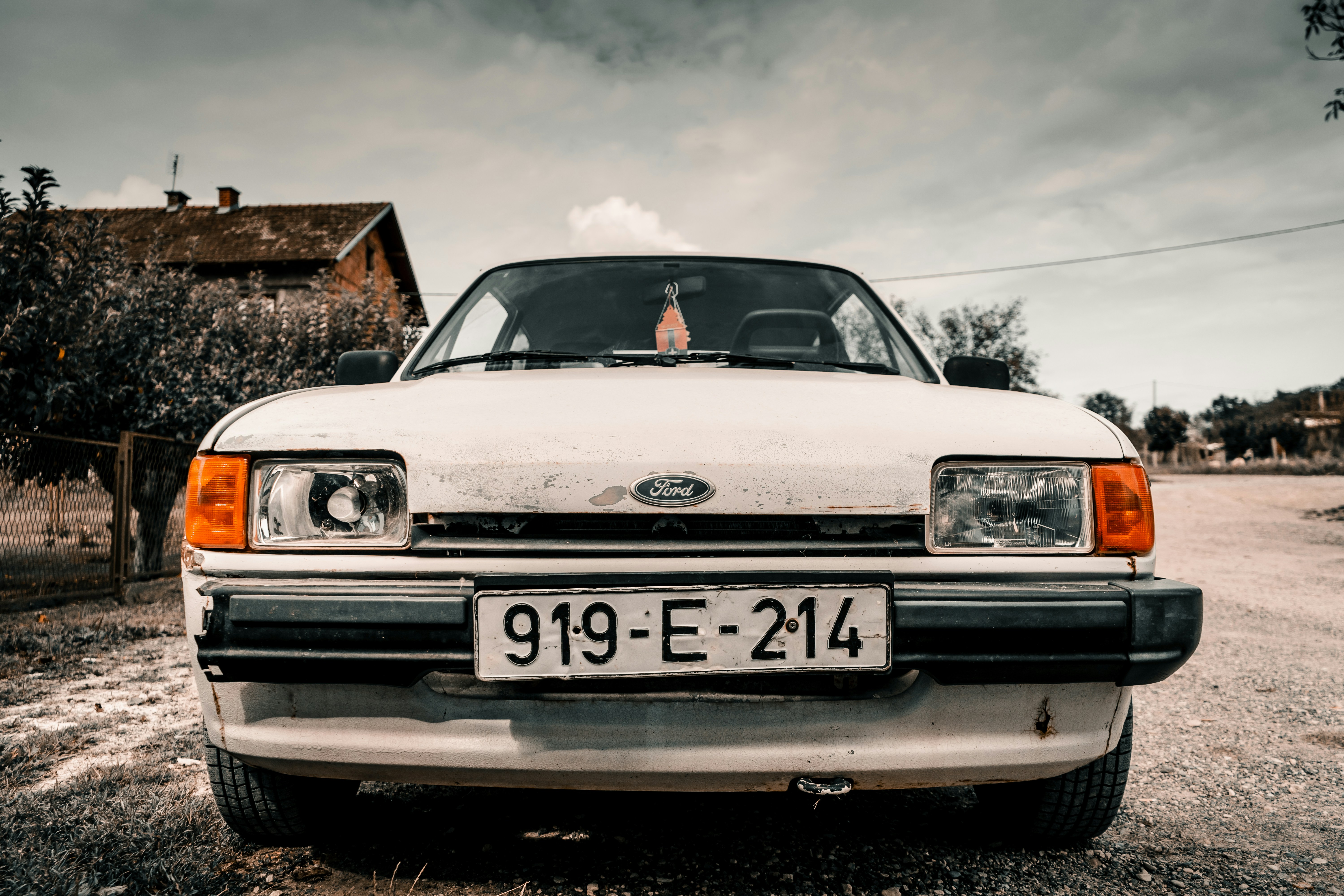 Vintage white car parked on a rural road with rustic buildings in the background.