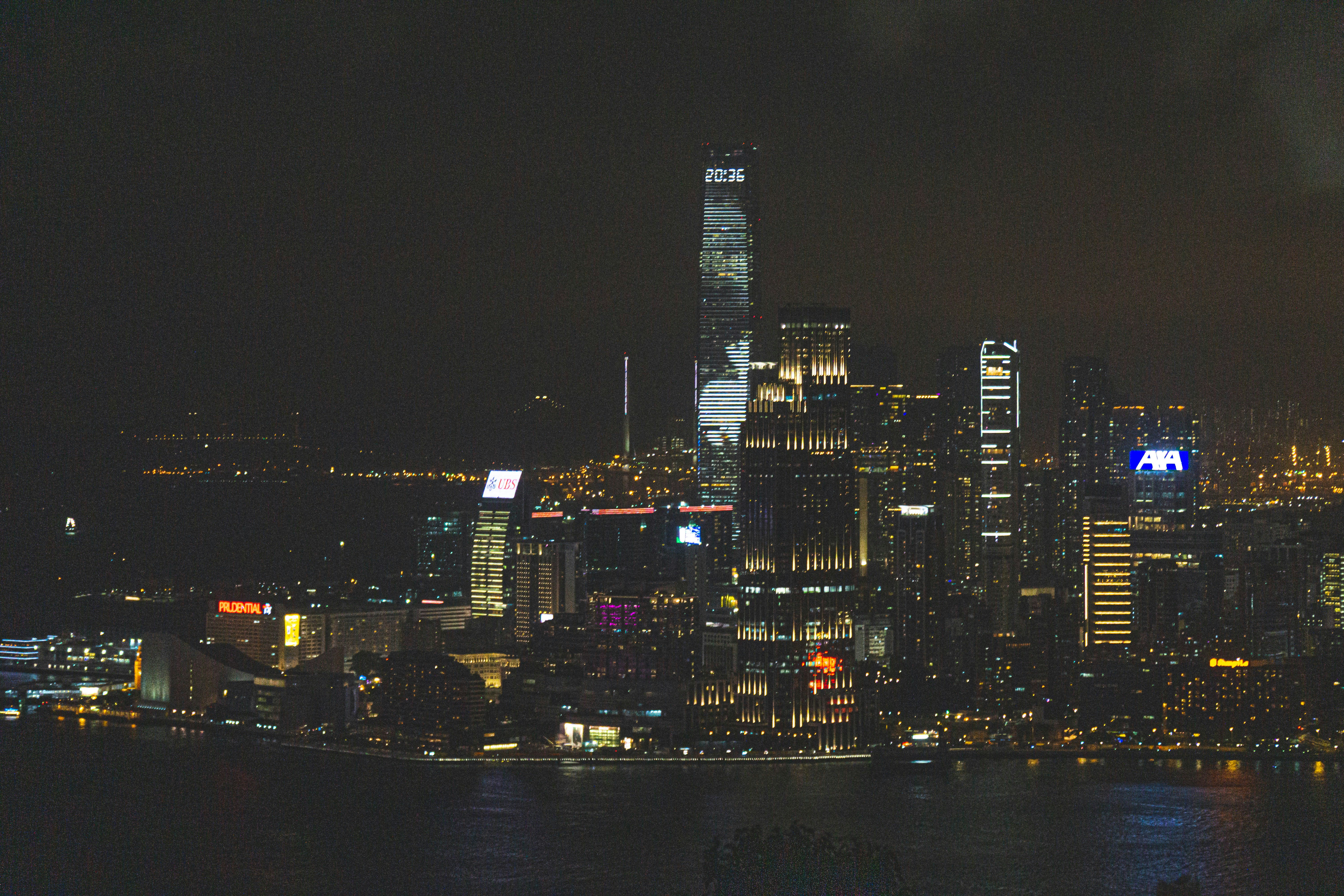 Illuminated skyline of a bustling city at night, showcasing towering skyscrapers and vibrant reflections on the water.