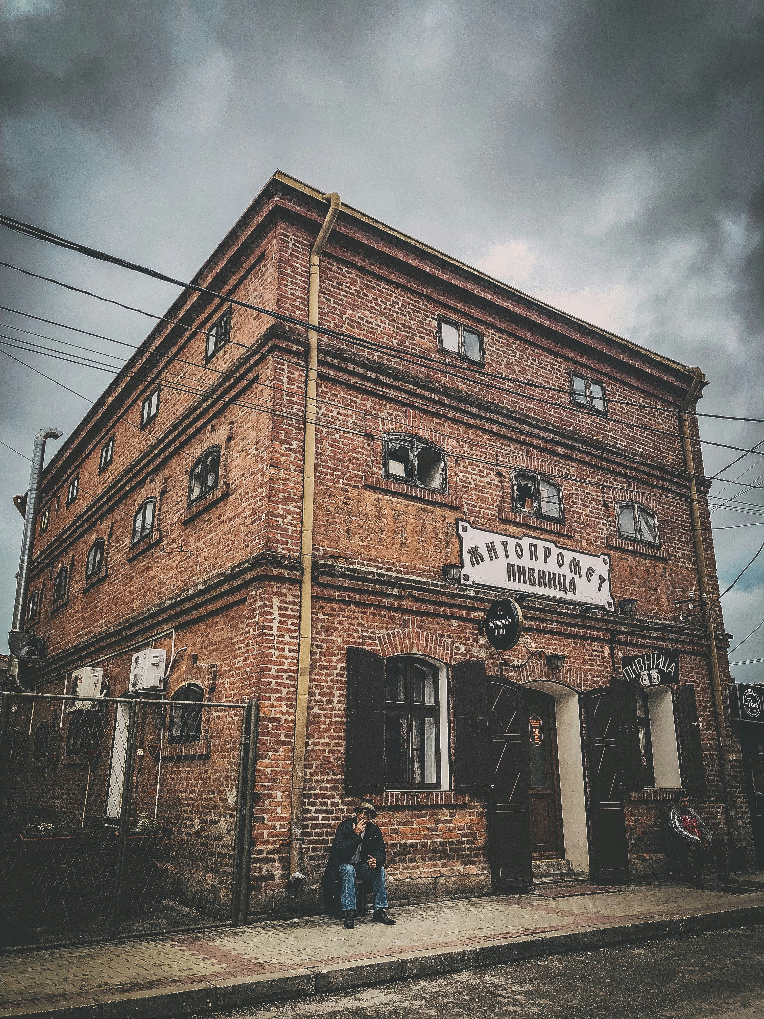 Old brick building, Čačak, Serbia  | man sitting in front of brown building during daytime