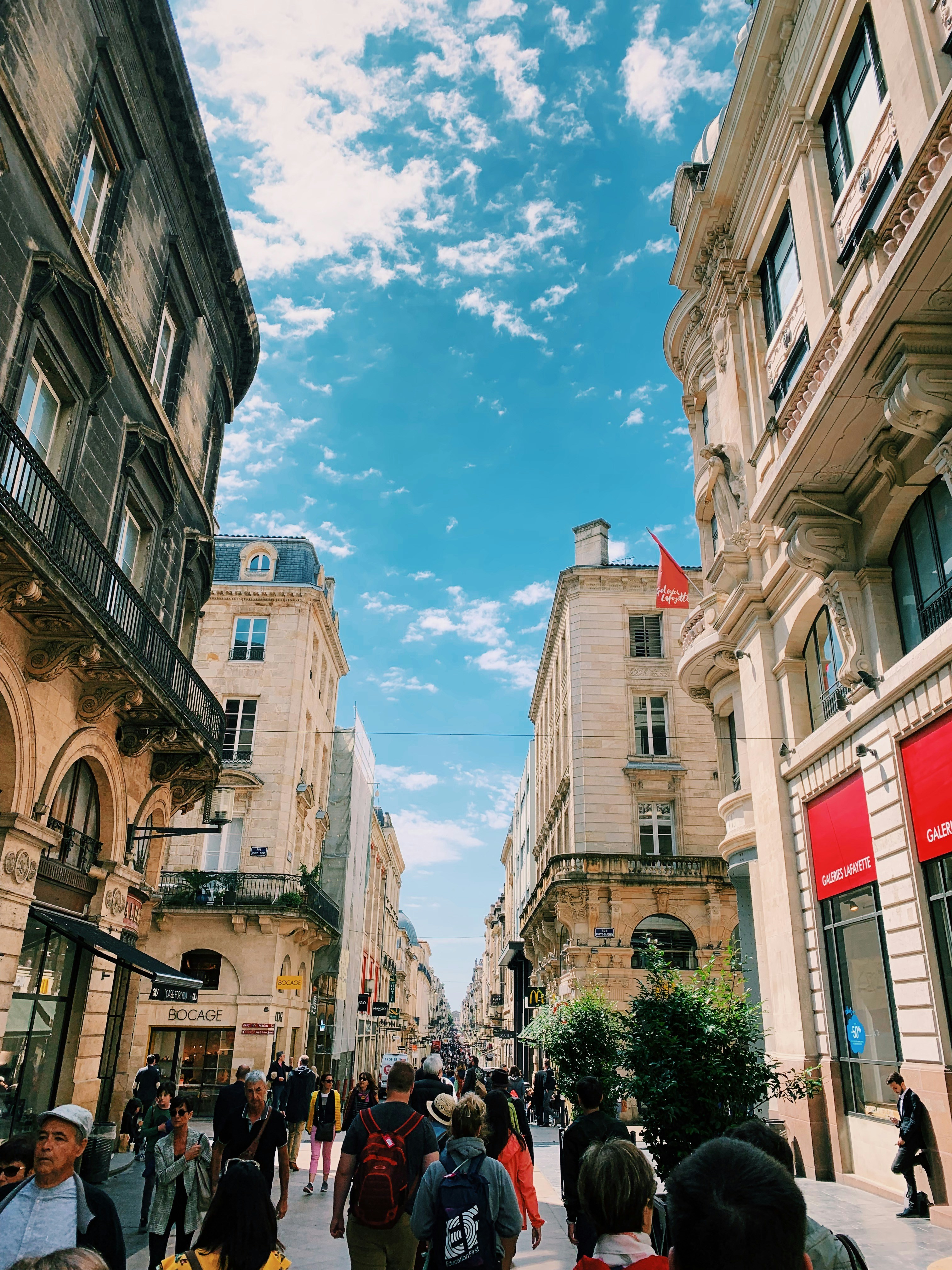 Bustling street scene in a historic district, framed by elegant architecture and a bright blue sky. The lively atmosphere captures the essence of urban life.