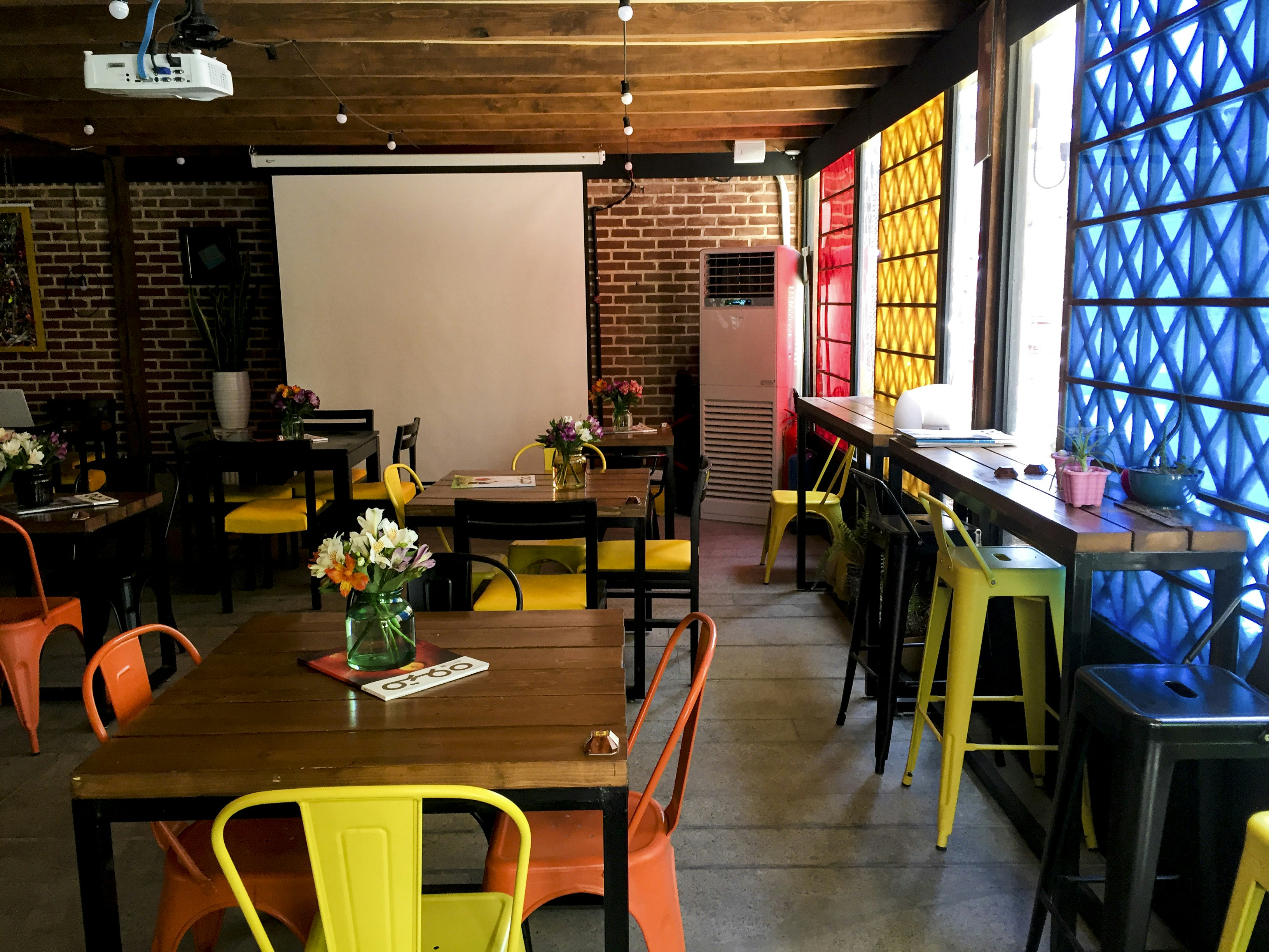 Brick-Walled Café: Rainbow Chairs, Soft Sunlight, and a Central Projection Screen